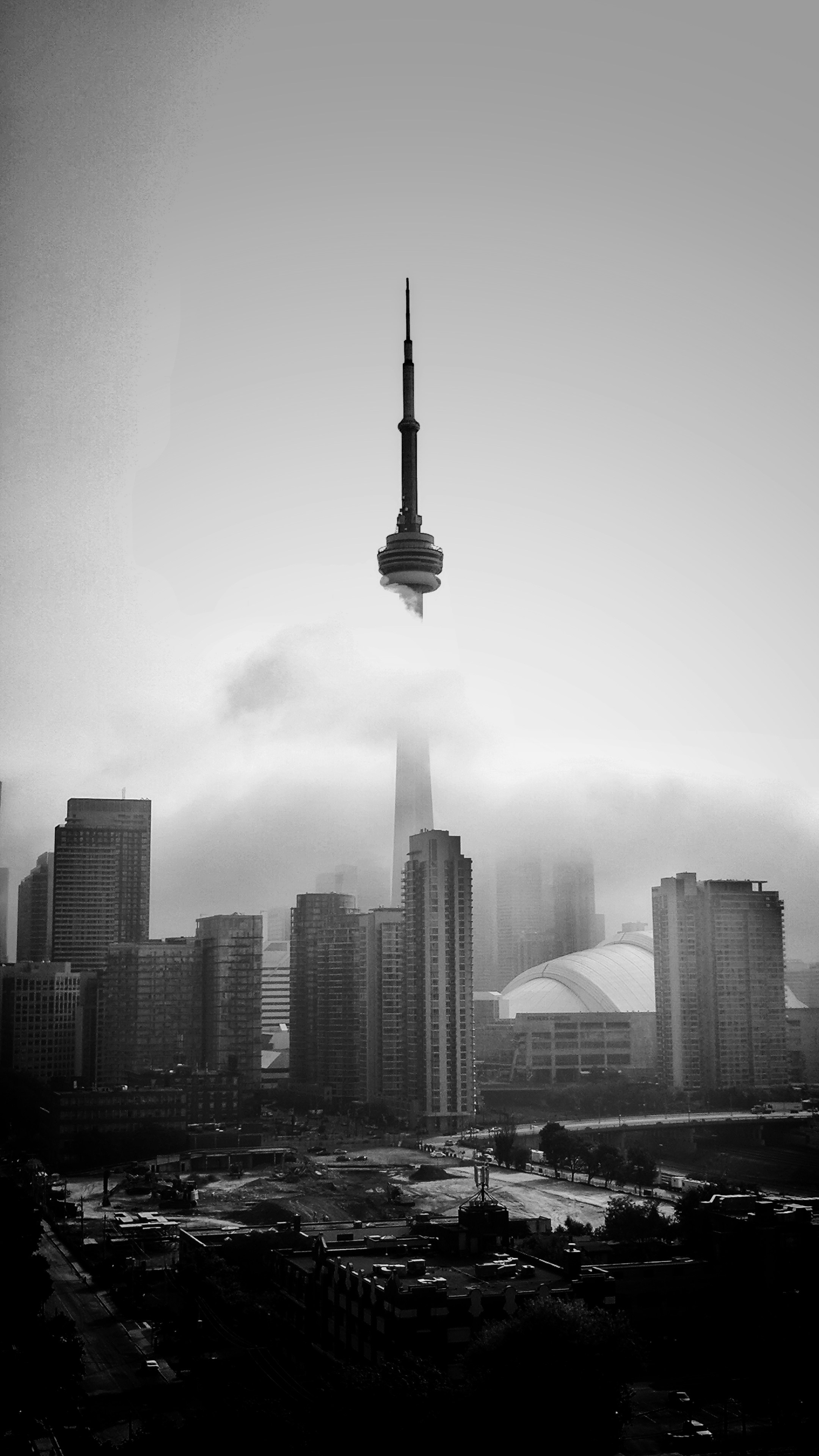 Black and white cityscape with a tower emerging through low-hanging fog.