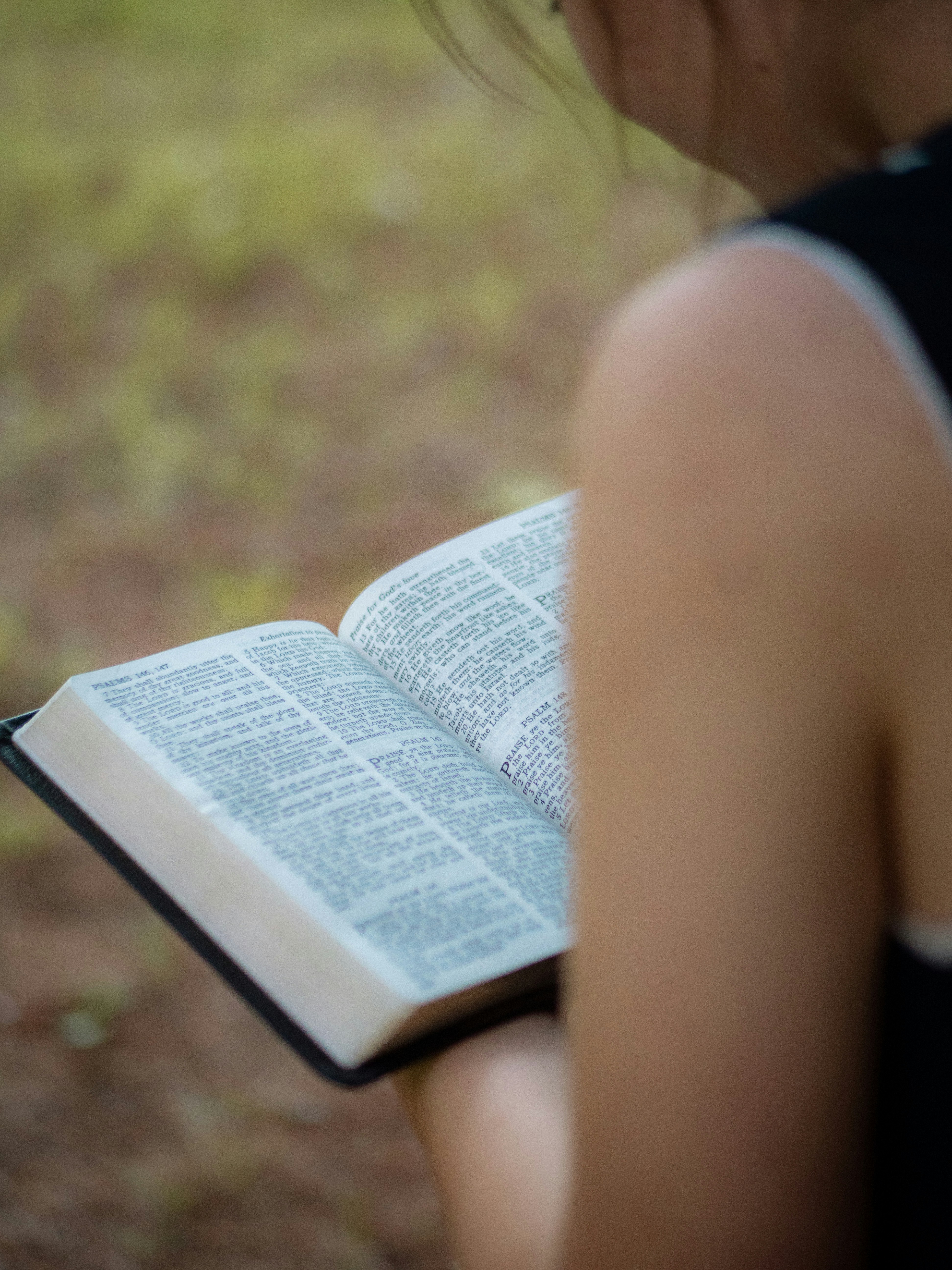 Person holds an open Bible outdoors, pages spread in the foreground, with a softly blurred natural backdrop.