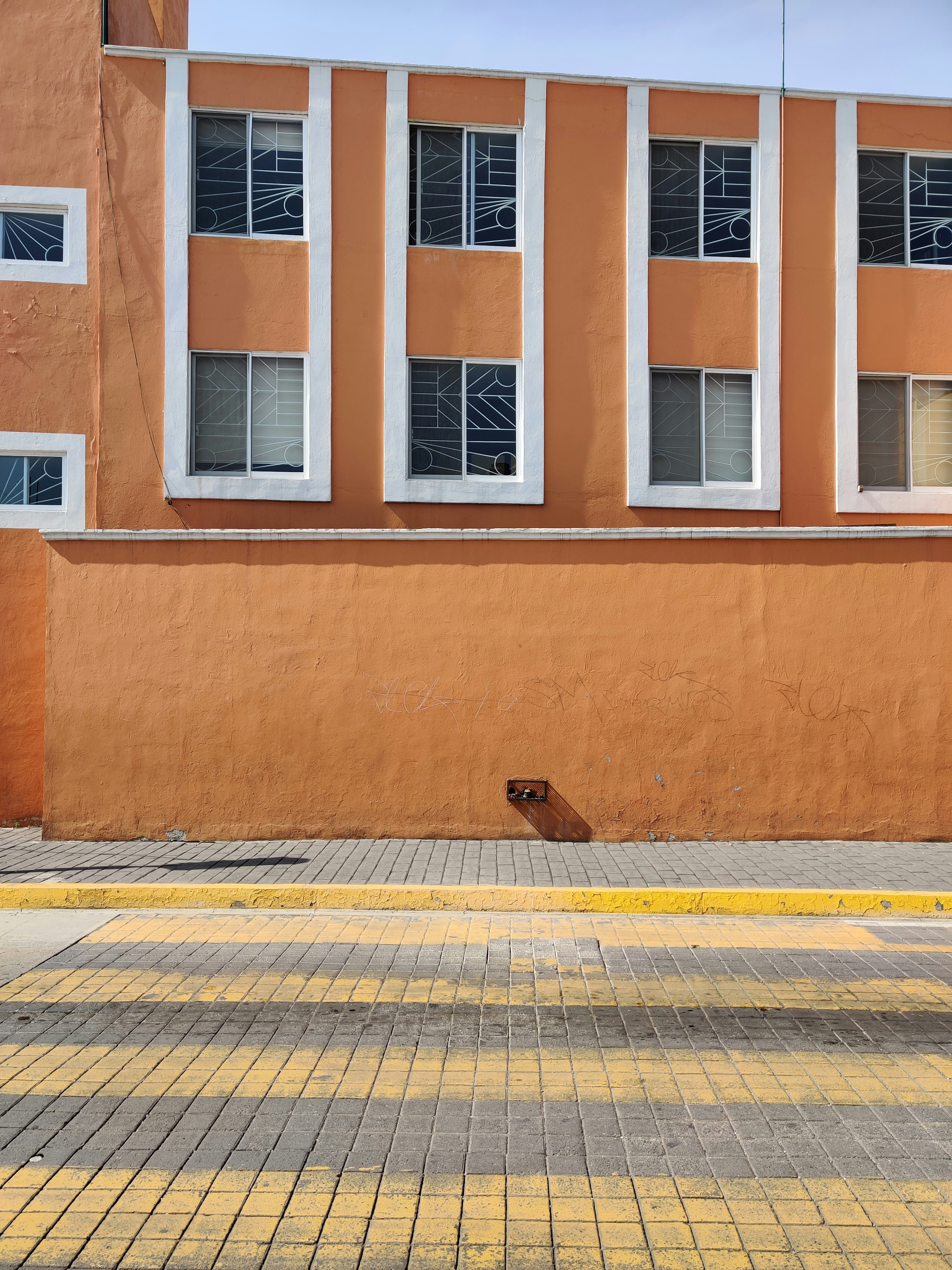 Orange building facade with grid-like windows above a yellow-striped pedestrian crossing.