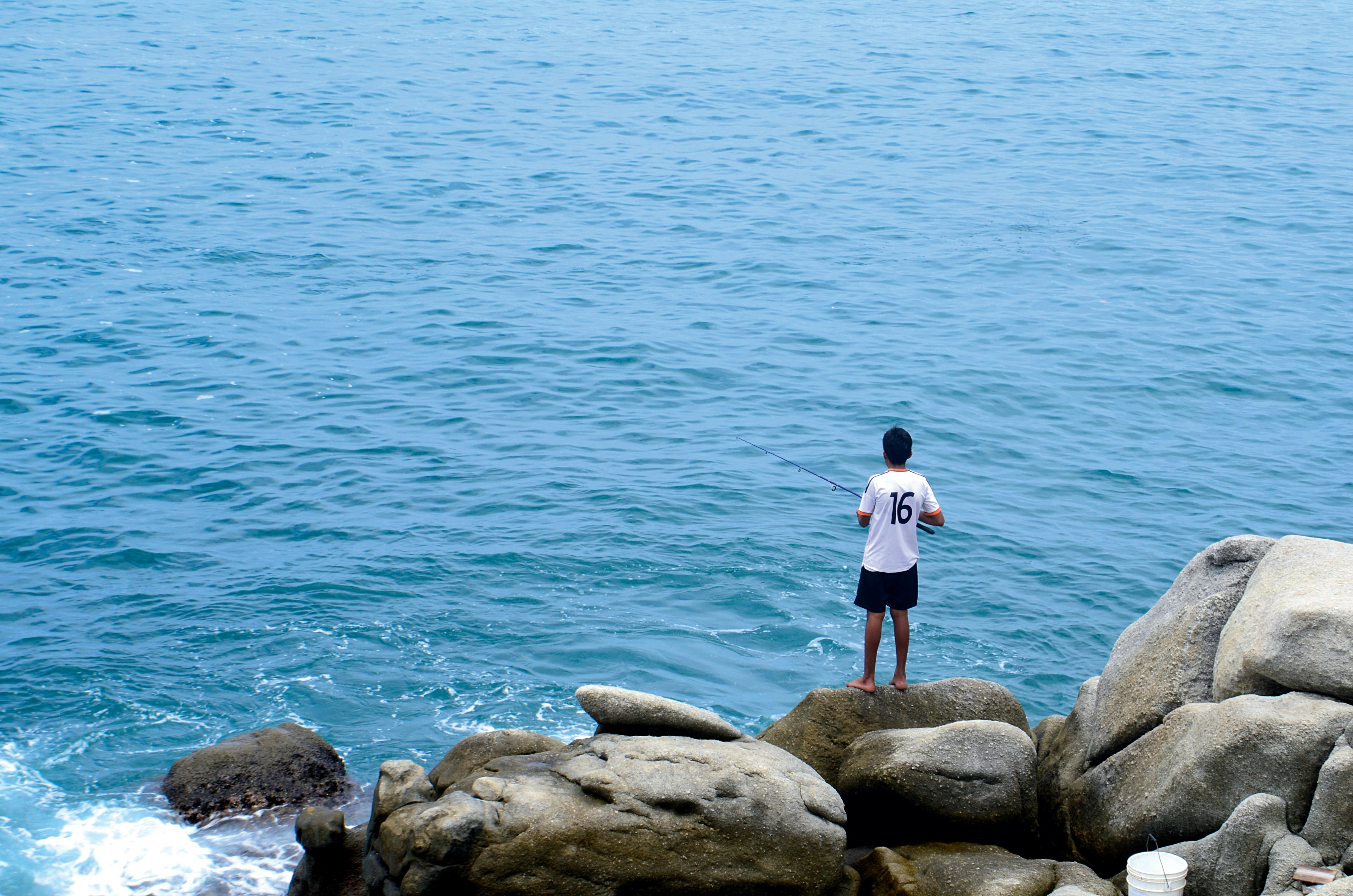 Sea-Edge Sentinel: Lone figure in a numbered jersey atop rugged seaside rocks