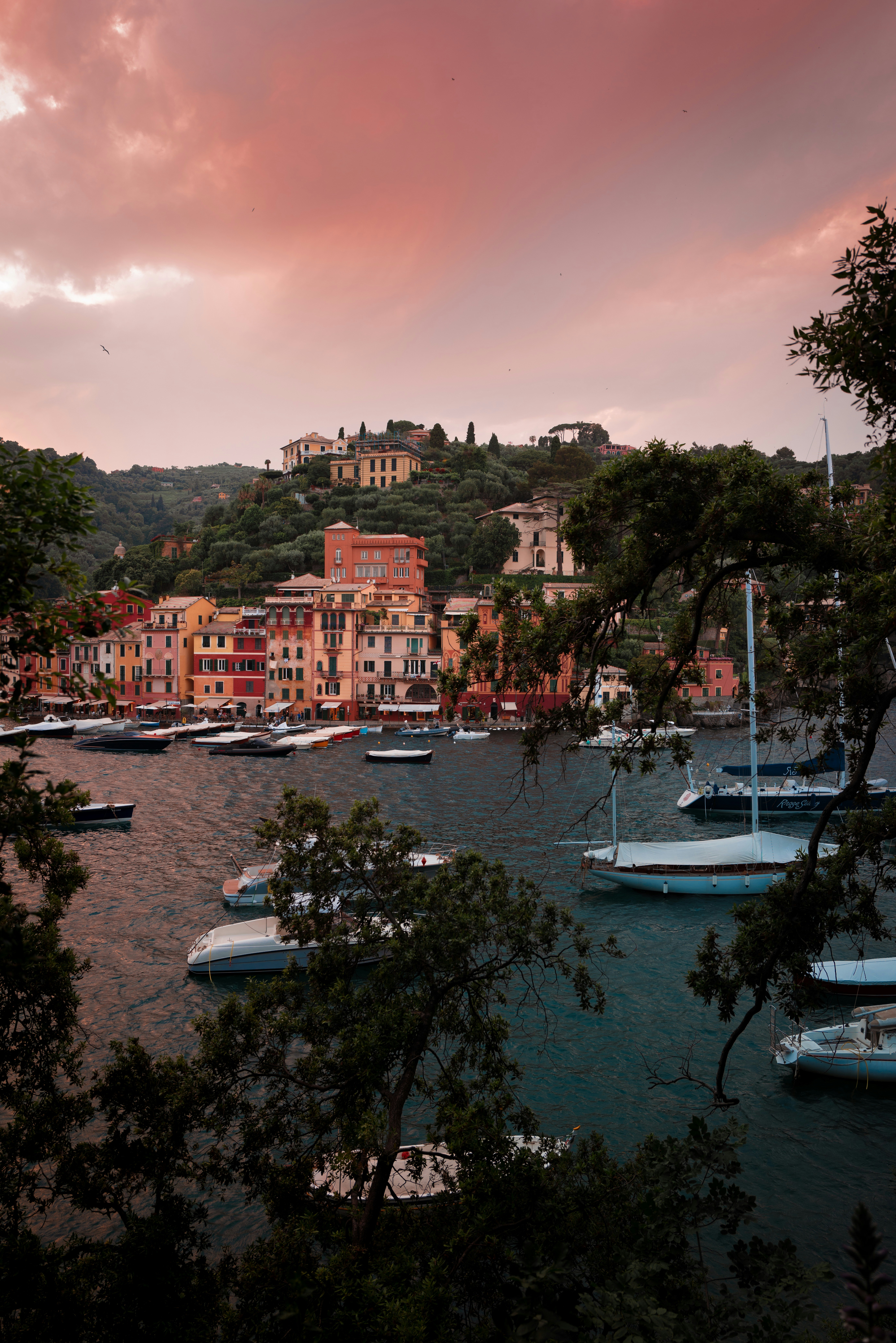 Vibrant coastal village nestled among lush hills, with colorful buildings reflecting in the tranquil waters at sunset.