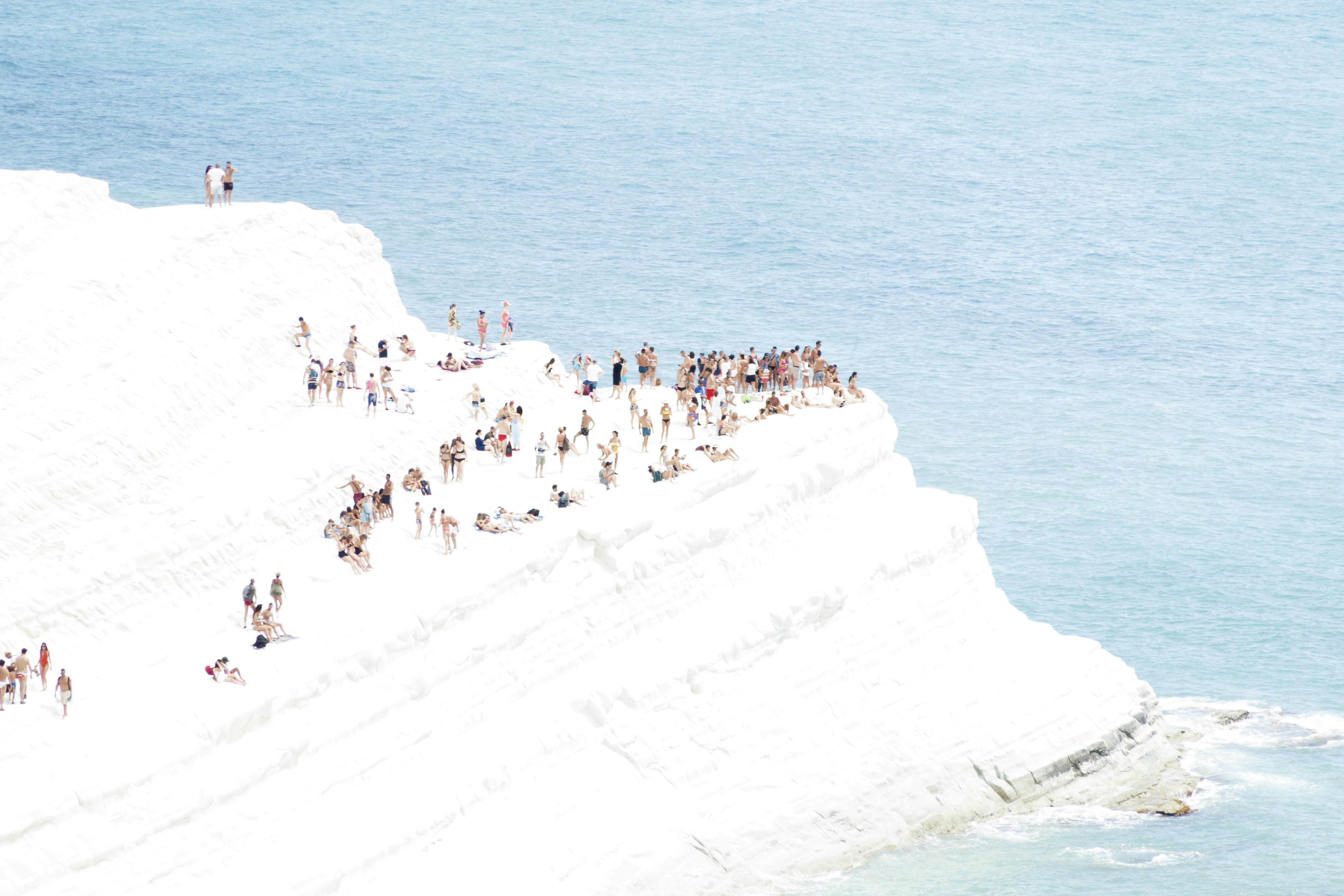 Crowds gather on the bright, sunlit white cliffs overlooking the blue sea.