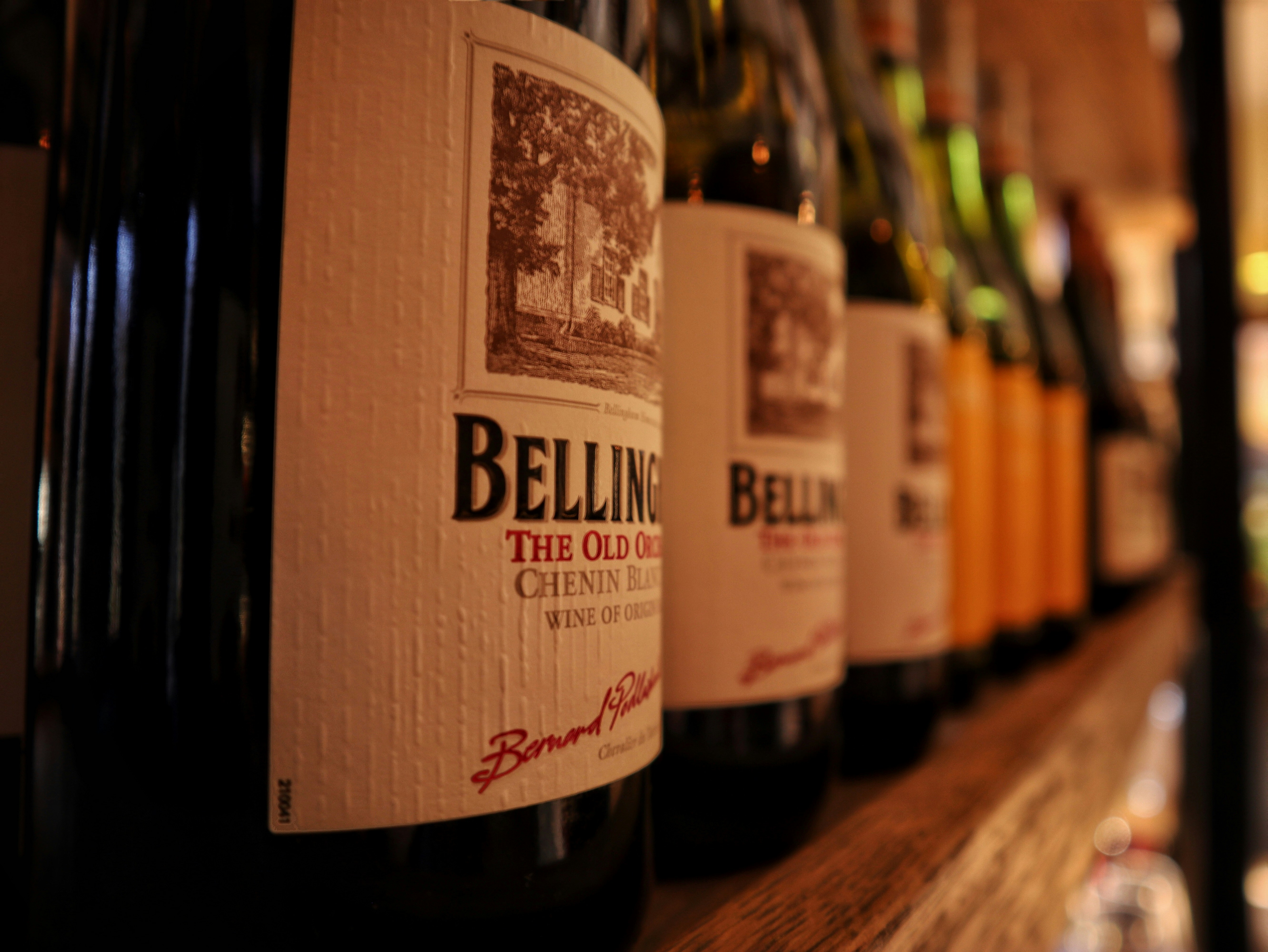 Wine bottles aligned on a wooden shelf in warm ambient lighting.