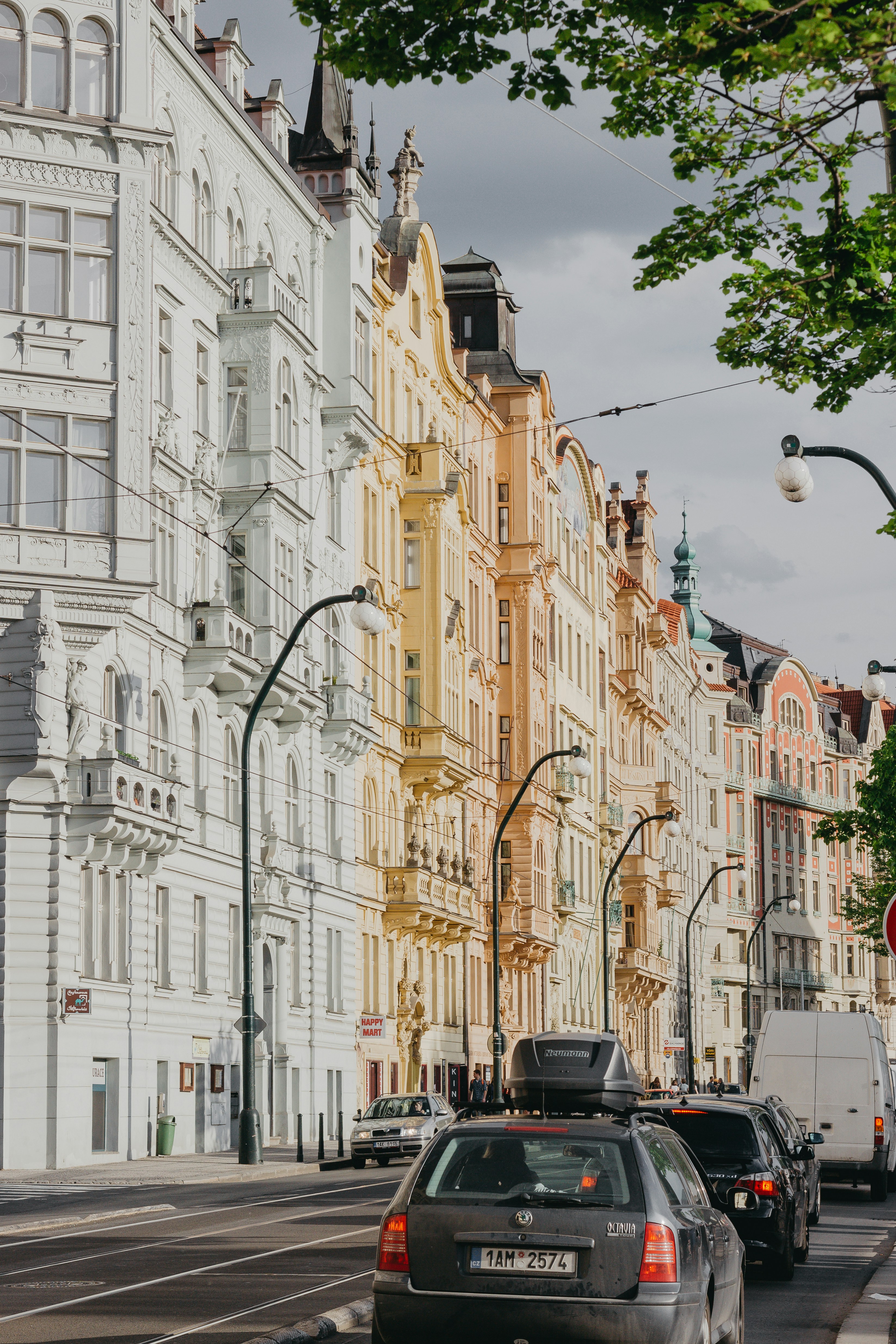 Colorful historic buildings line a bustling street, showcasing intricate architectural details under a cloudy sky.