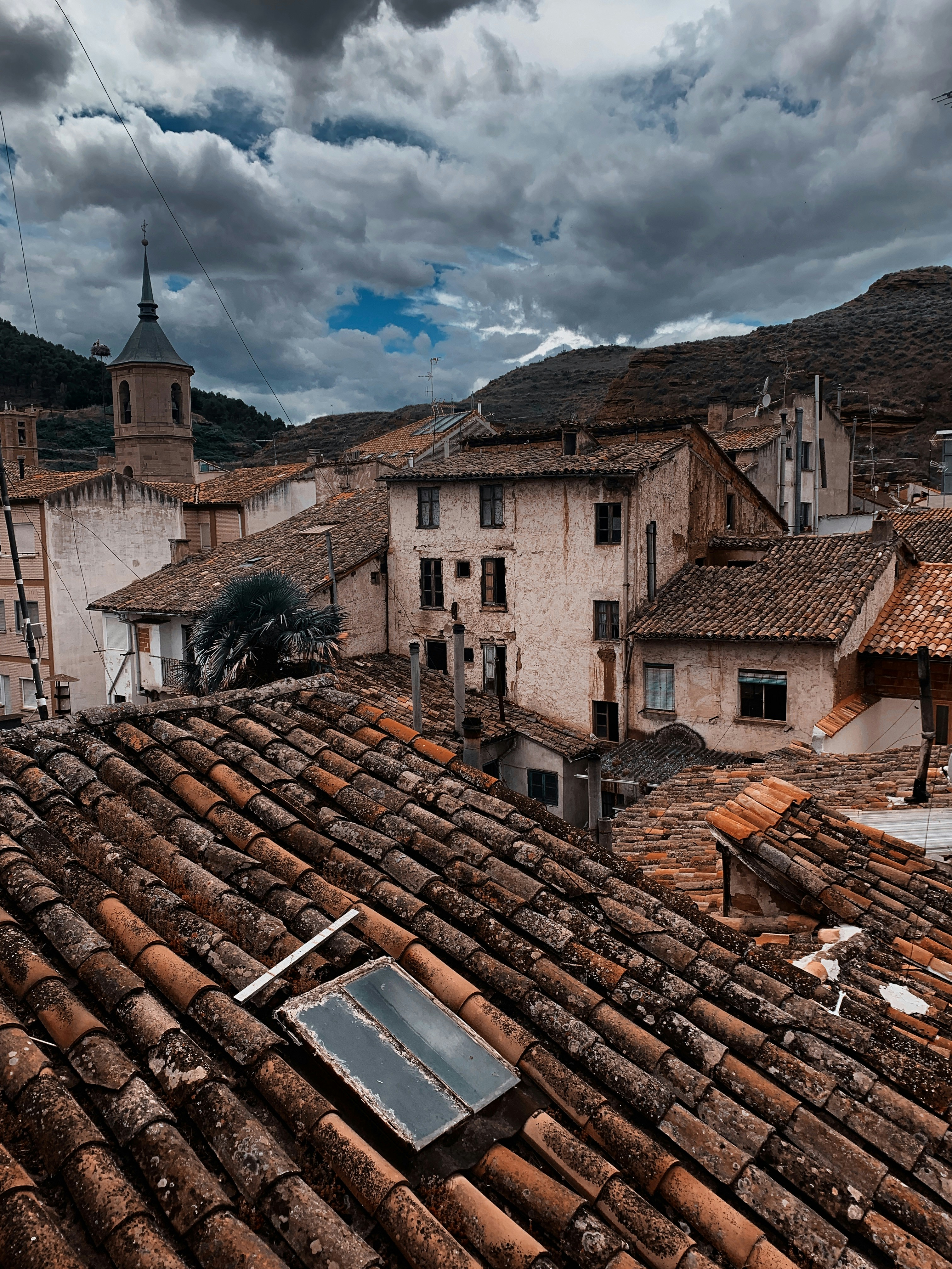 Aerial perspective showcasing rustic rooftops and historical buildings under a dynamic sky. The scene captures the essence of a quaint town steeped in history.