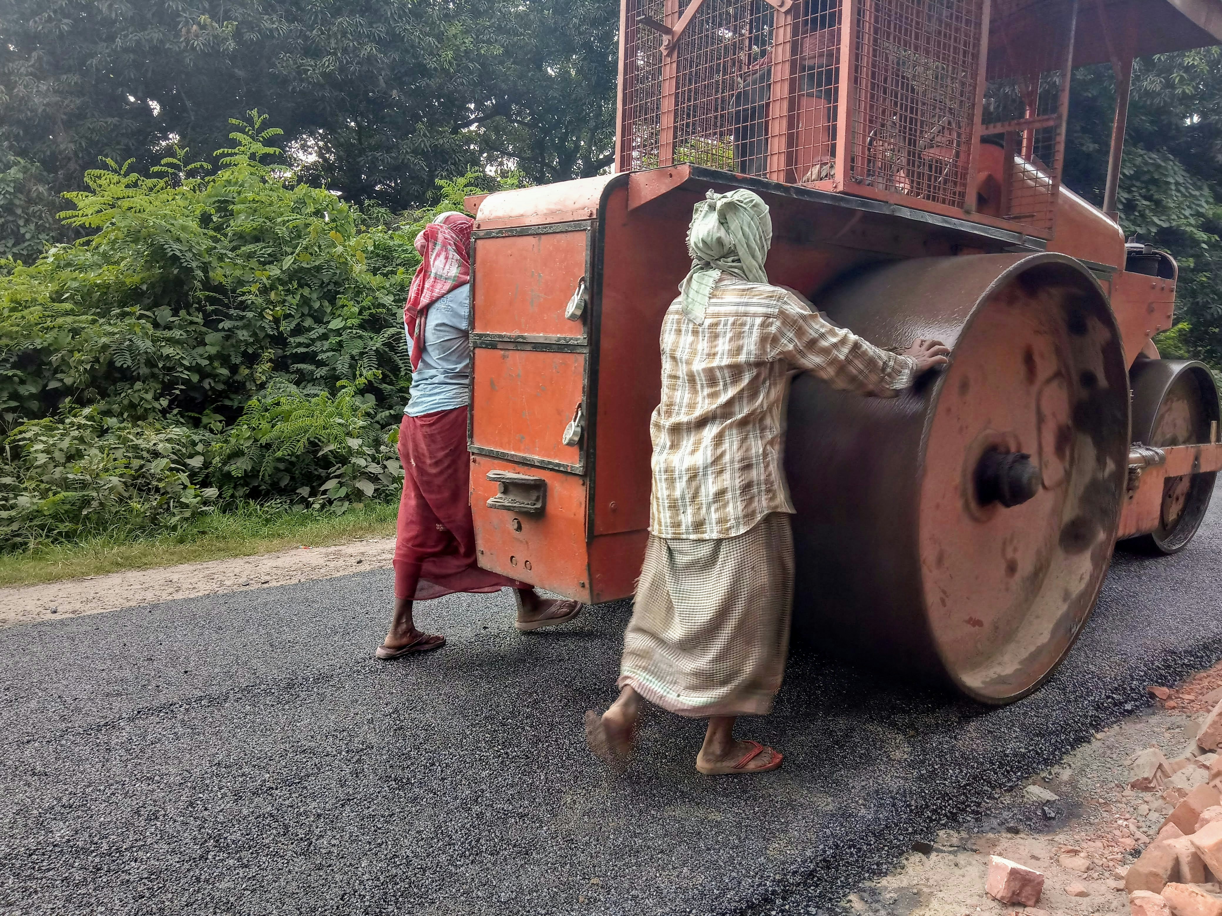 Coordinated Push: Two Labourers Maneuver a Rusty Road Roller