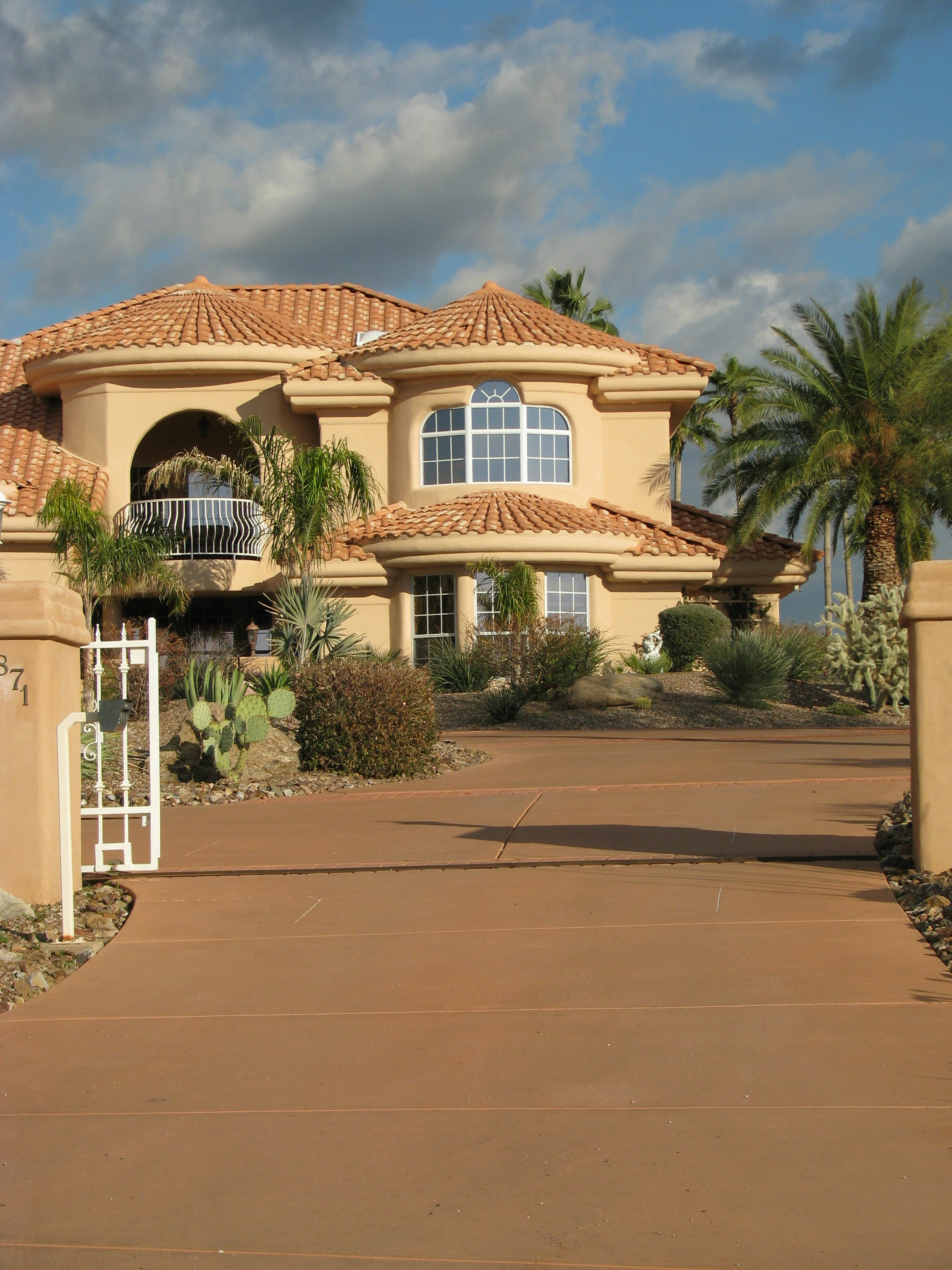 Elegant two-story home with a terracotta roof, surrounded by desert landscaping and palm trees.