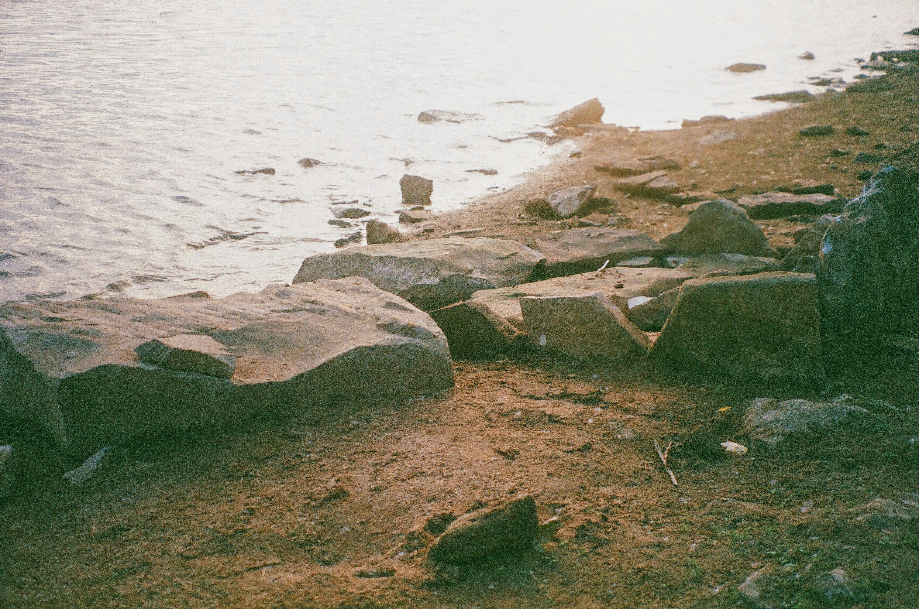 Rugged rocks line the sandy bank of a tranquil waterway, reflecting the soft hues of a fading day.