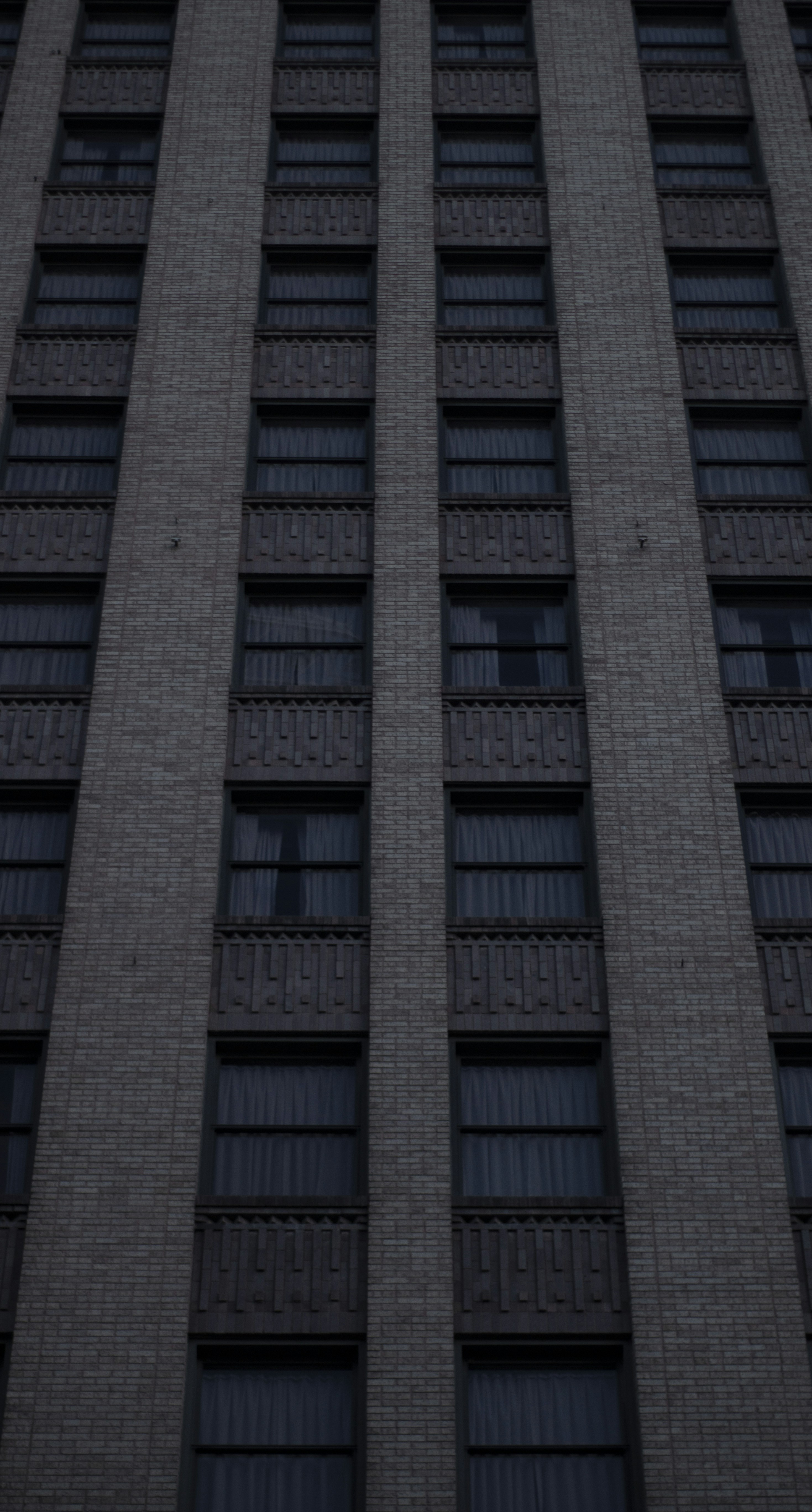 Architectural facade showcasing a rhythmic pattern of windows and textured brickwork, emphasizing vertical lines and muted tones.