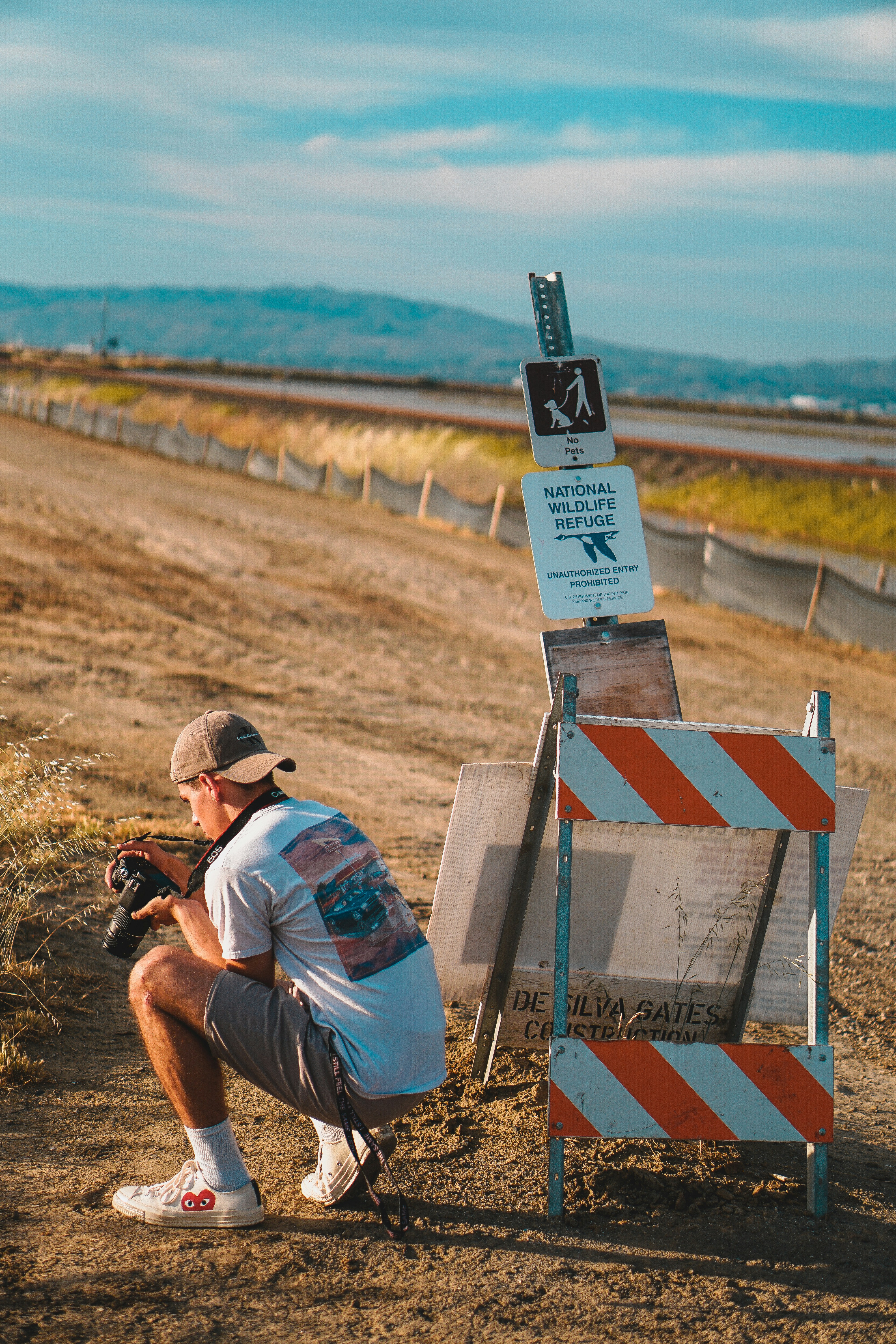 A photographer crouches near a wildlife refuge sign, focusing intently on capturing the surrounding nature. Signs of conservation efforts are prominently displayed.