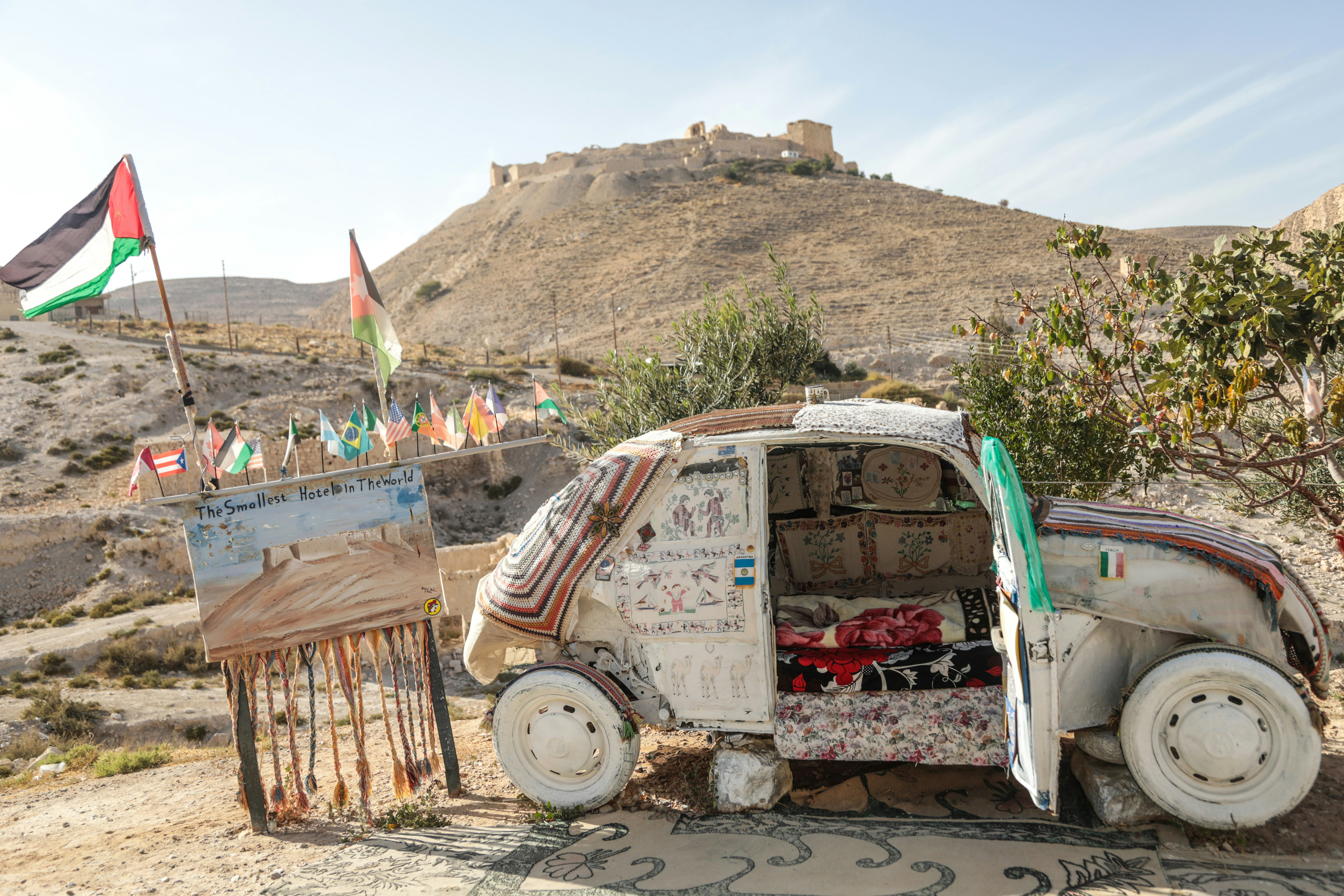 Desert Shrine: A weathered radio-car and flags under a hilltop fortress