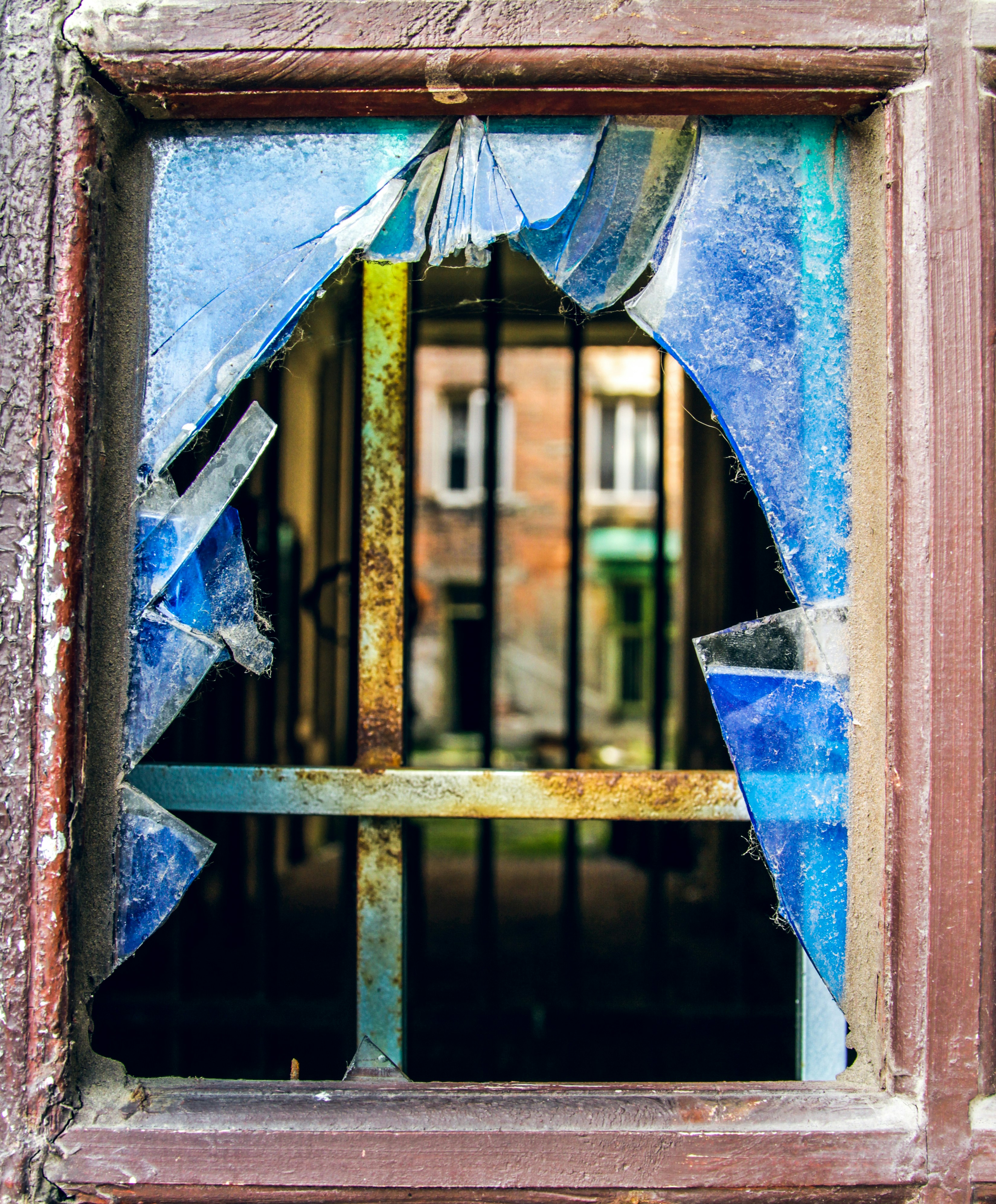 Fragmented Blue Window: Rusted Bars Framing a Dim Interior