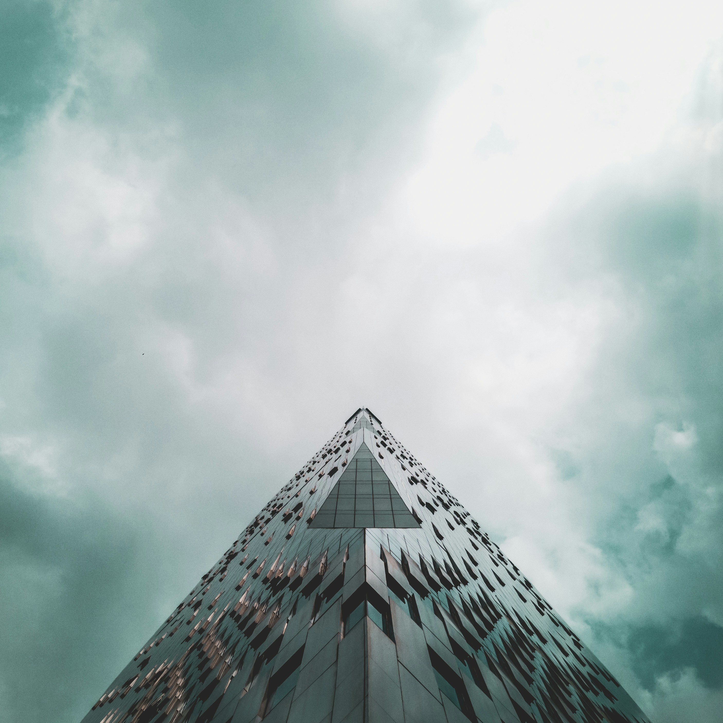 A low-angle photograph of a tall glass-and-steel pyramid rising toward a moody turquoise sky.