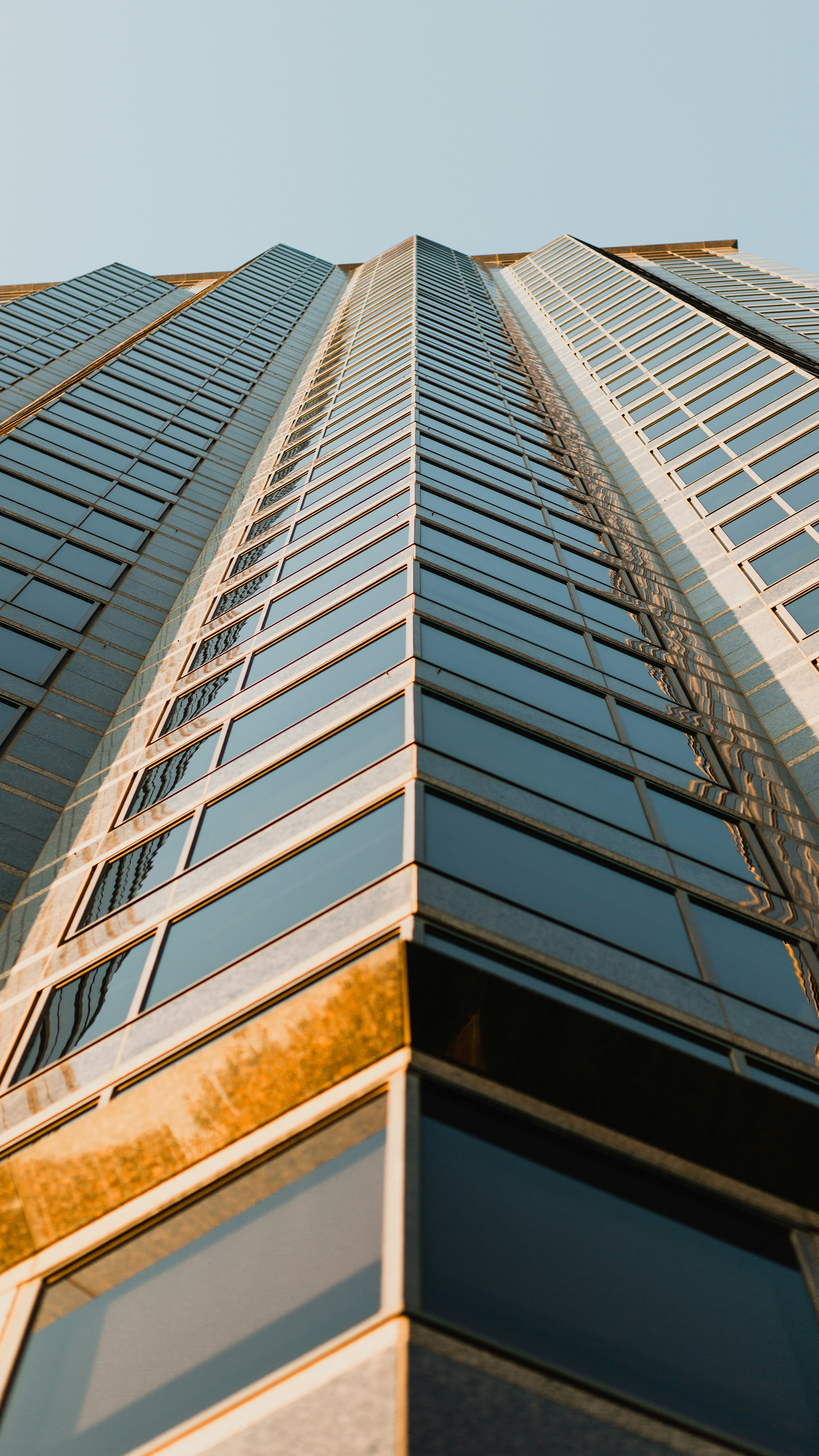A towering skyscraper viewed from below, showcasing its sleek glass facade and geometric patterns against a clear sky.