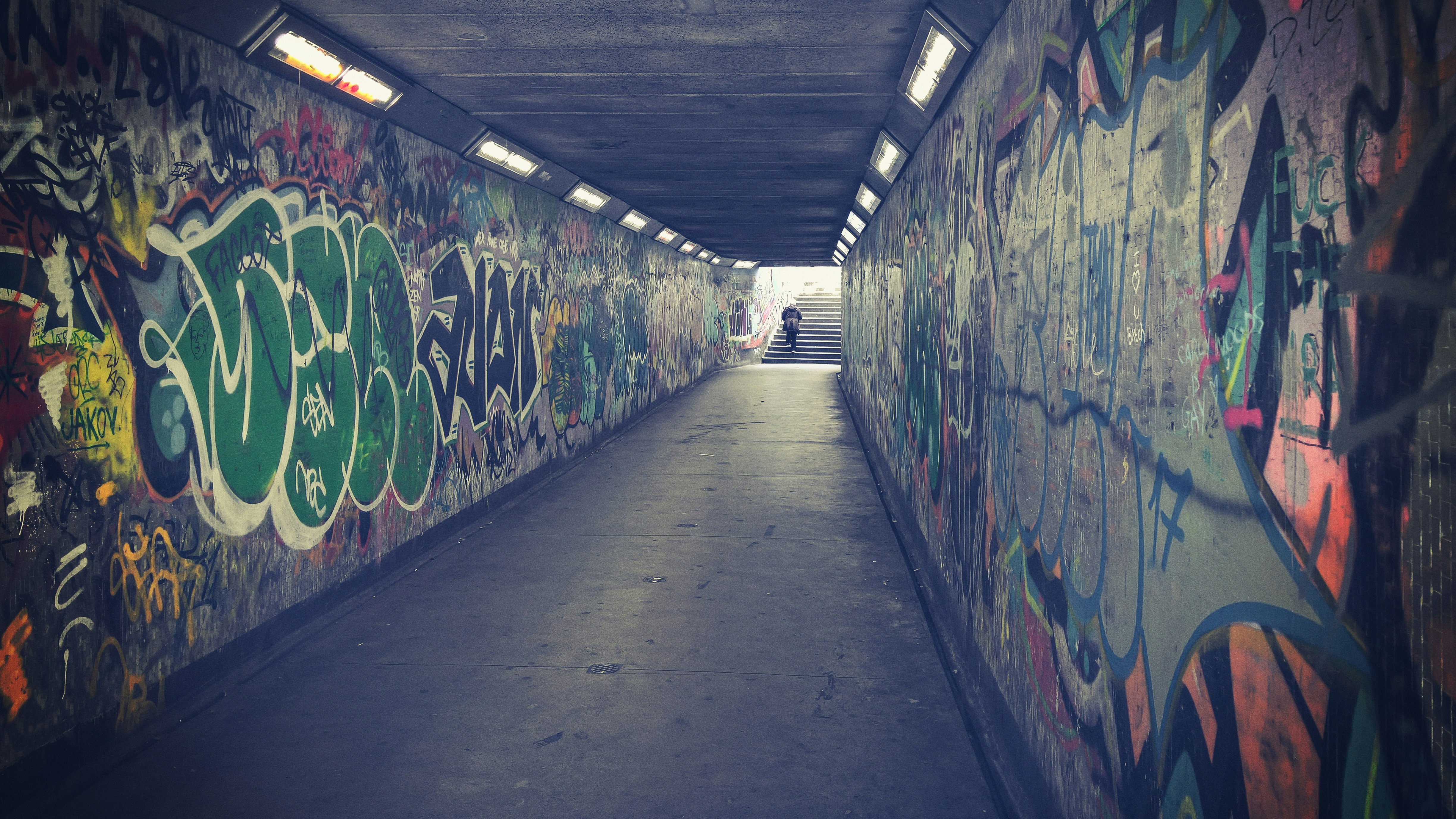 Vibrant graffiti adorns the walls of a dimly lit urban tunnel, leading to a staircase that hints at the world beyond. The scene captures the essence of street art and urban exploration.