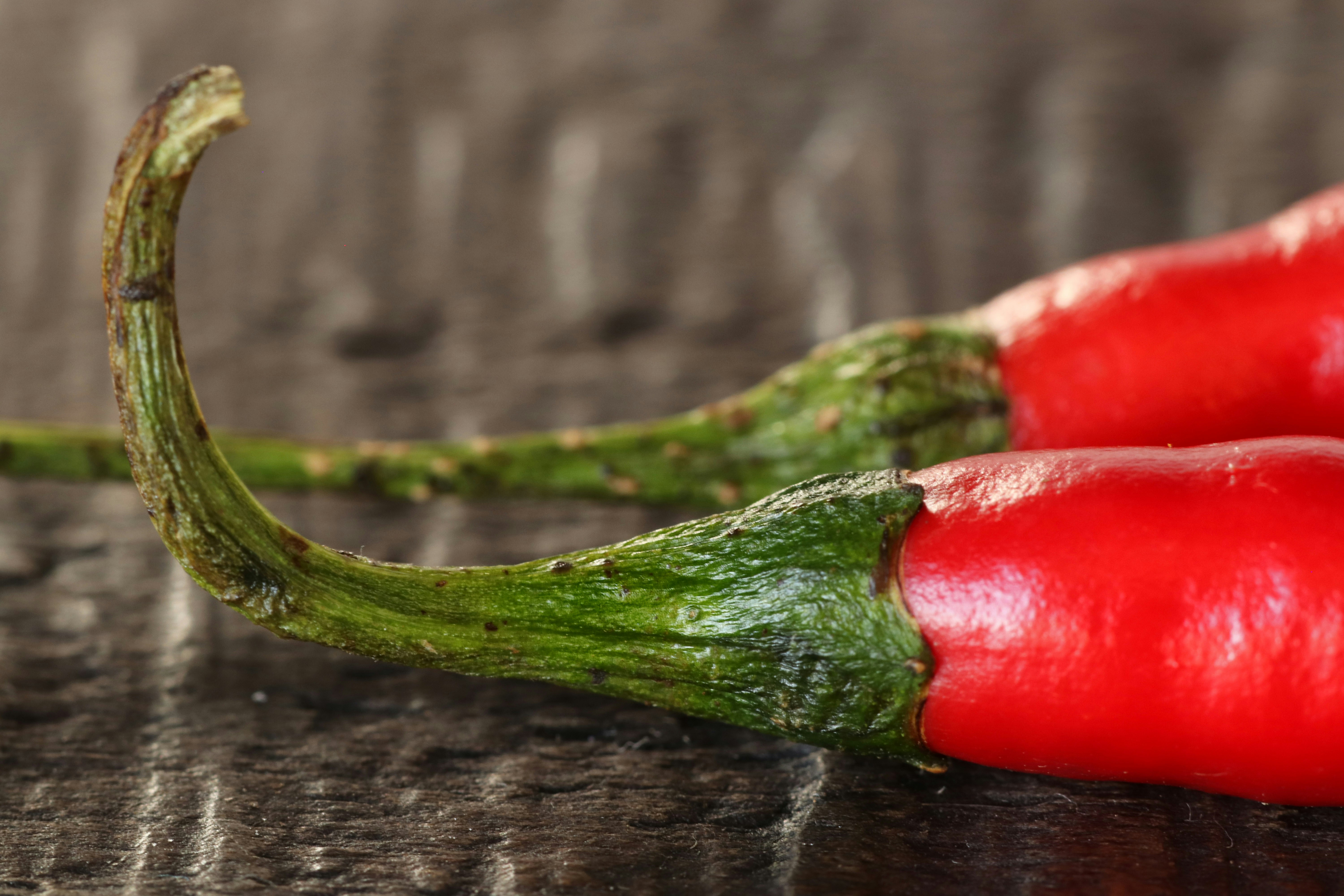 Close-up of vibrant red chili peppers with distinctive green stems on a dark wooden surface.