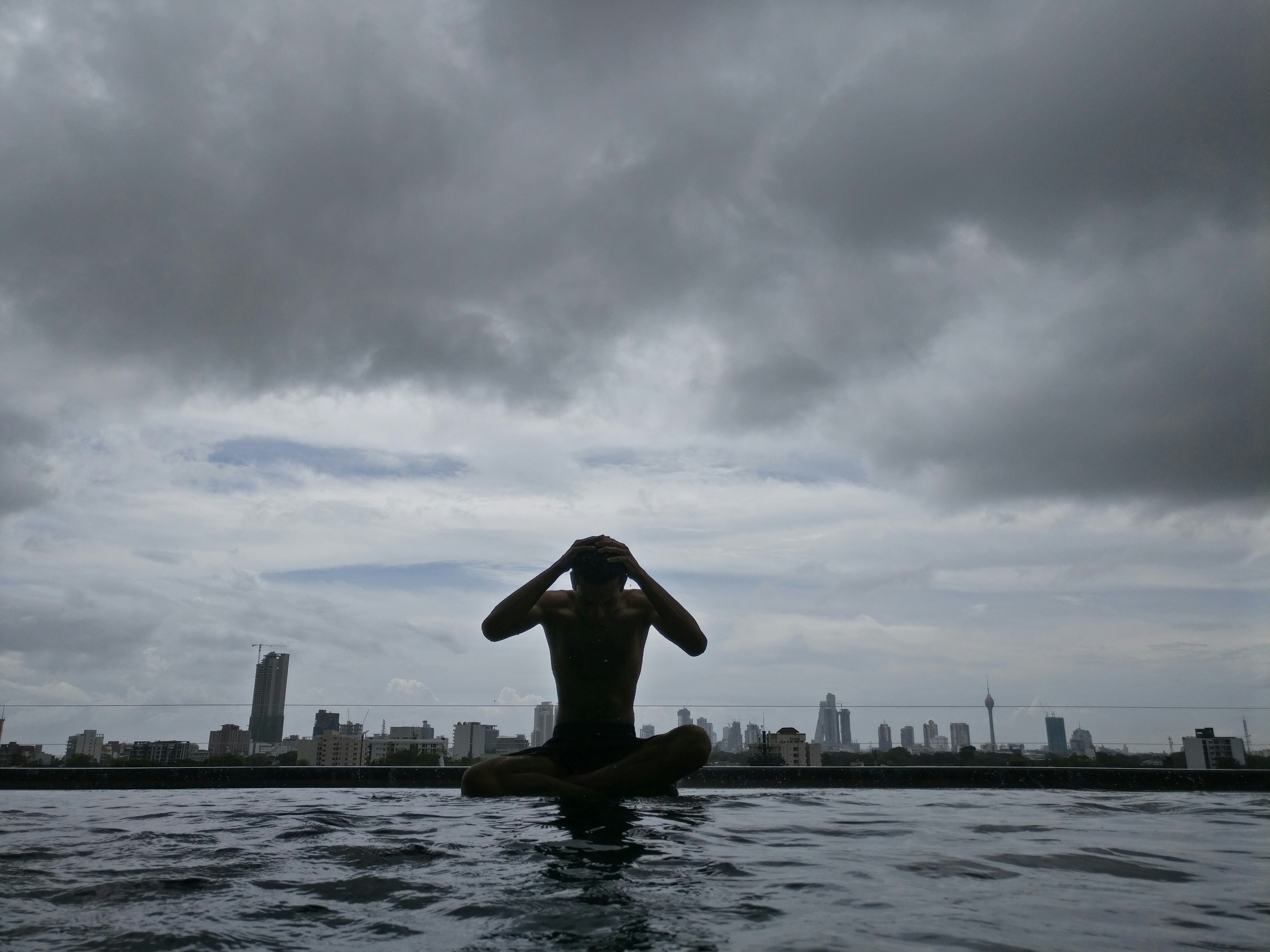 Silhouette of a person meditating on water with a city skyline under dramatic clouds.