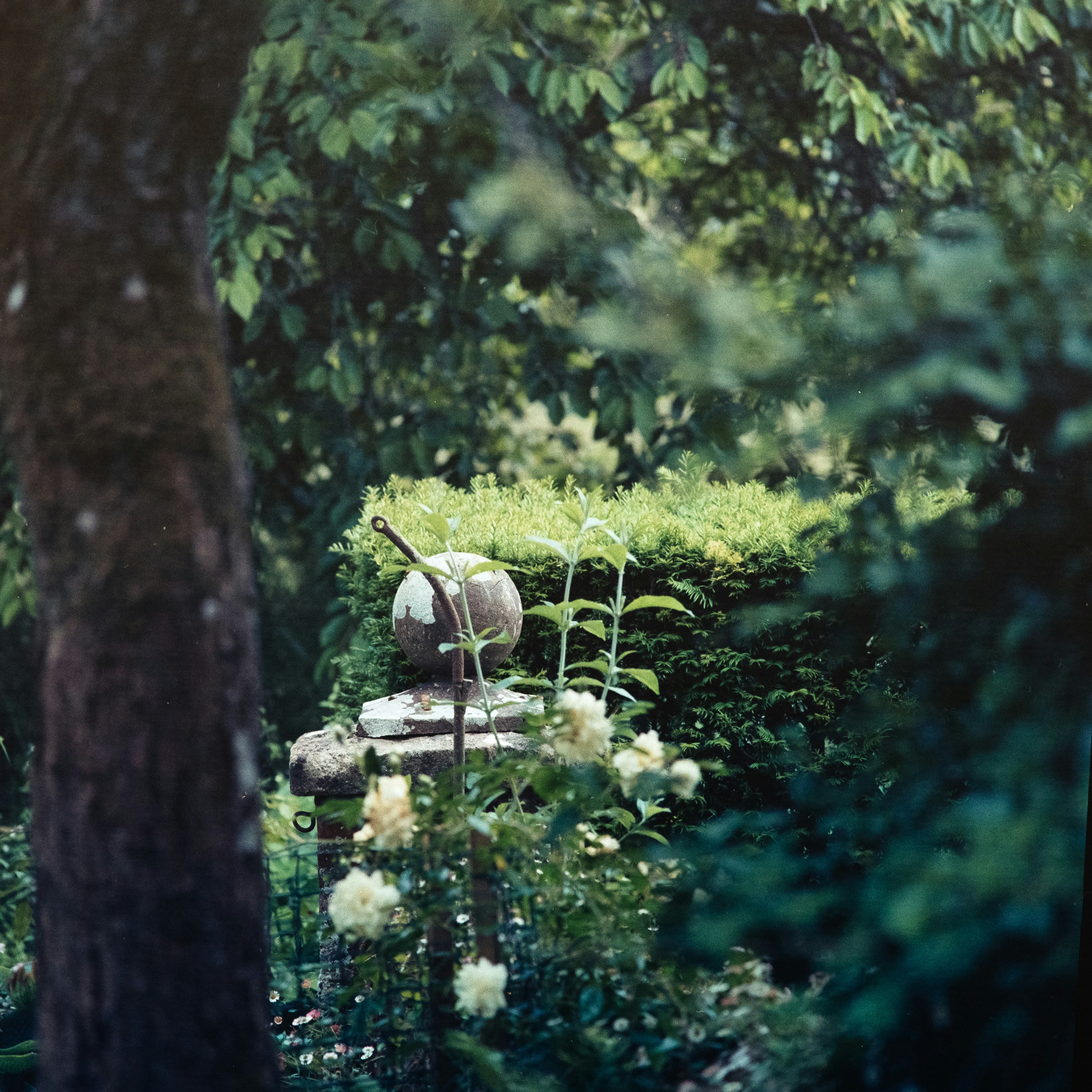 A tranquil garden scene featuring a stone sculpture amidst lush greenery and blooming flowers, inviting contemplation.