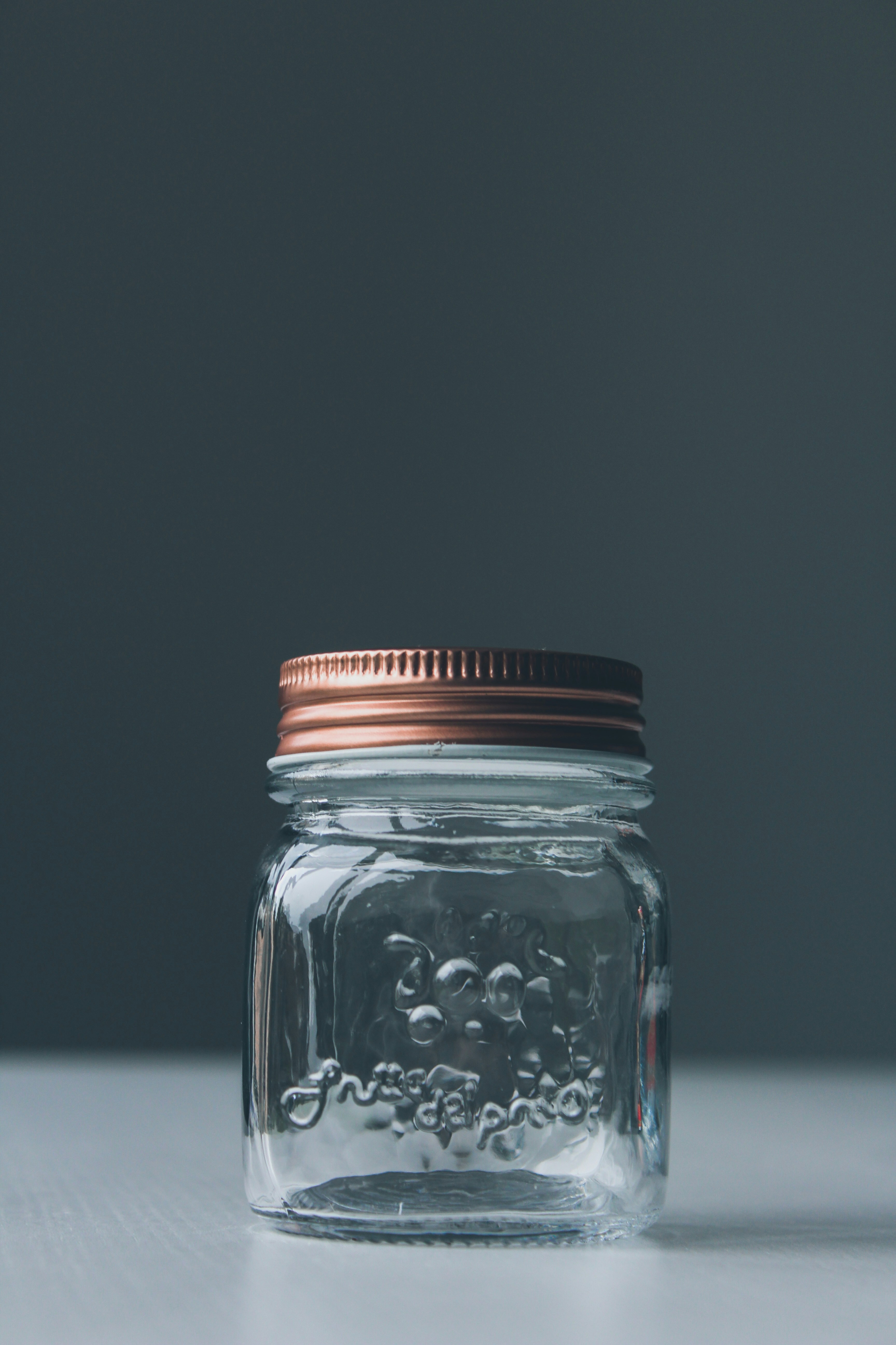 Clear glass jar with a copper lid resting on a light surface against a muted background.