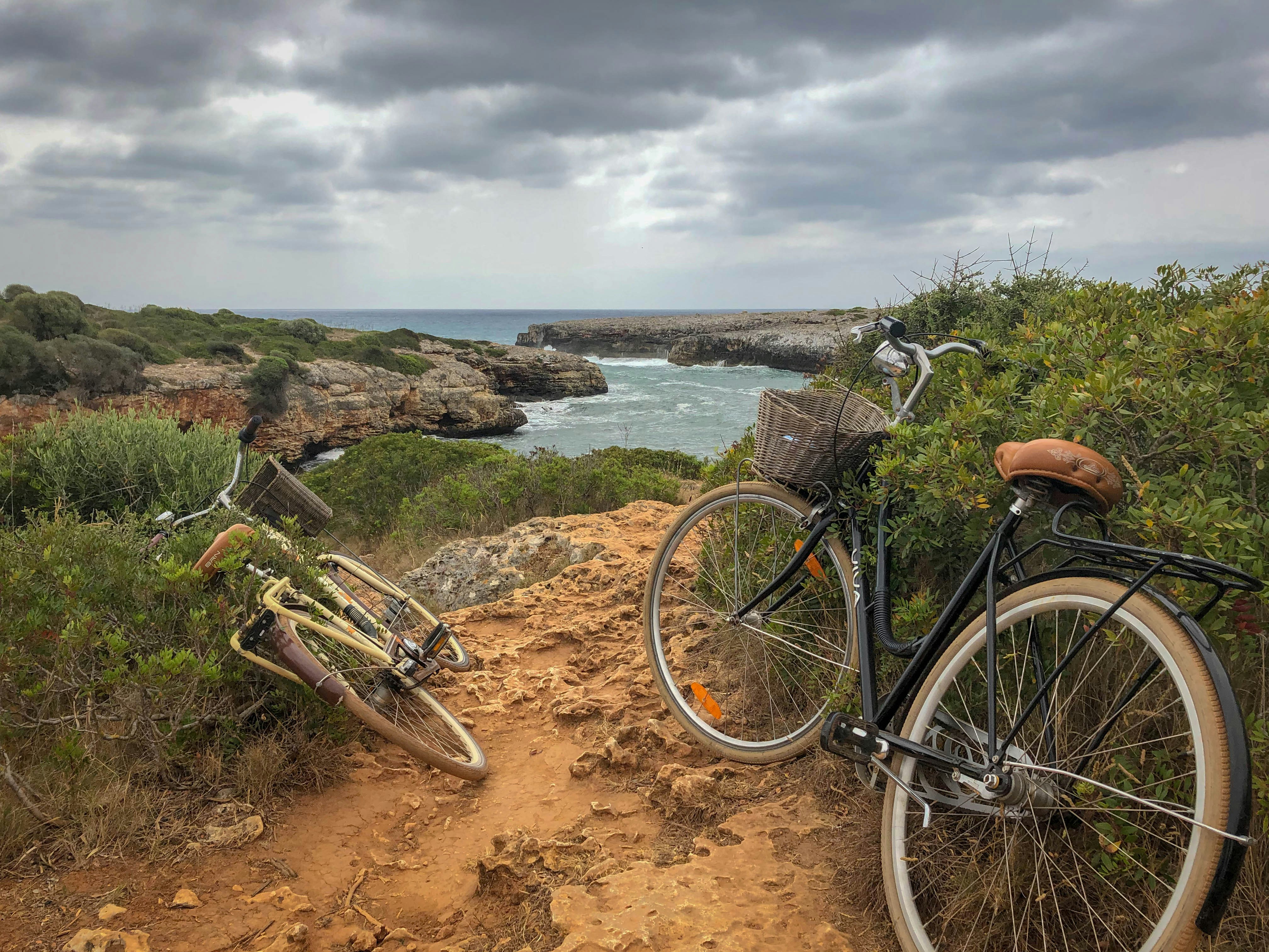 Two Bikes Rest on a Rust-Colored Coastal Trail Beneath Stormy Skies
