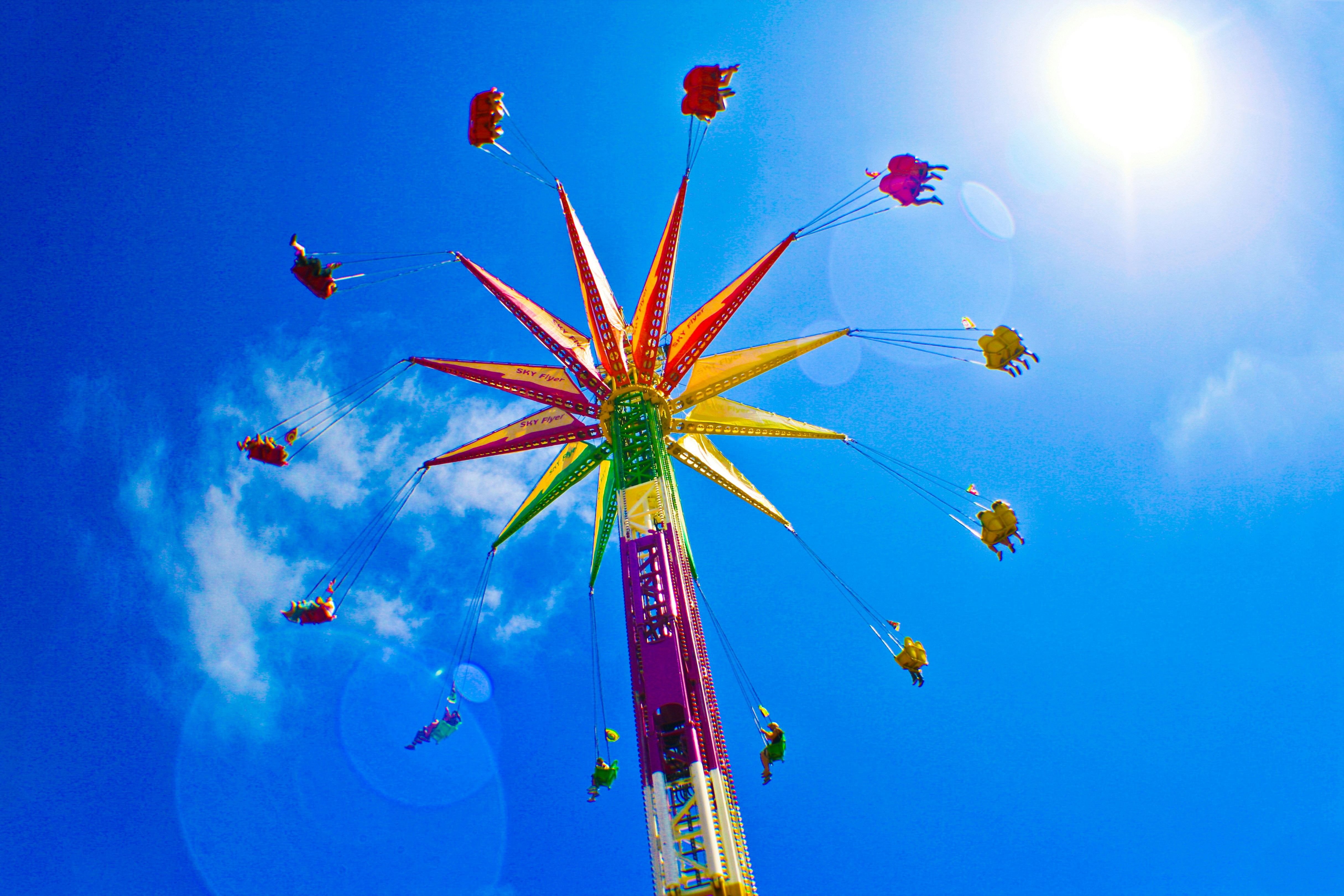 Colorful amusement park ride with suspended seats spinning under a clear blue sky and bright sun.