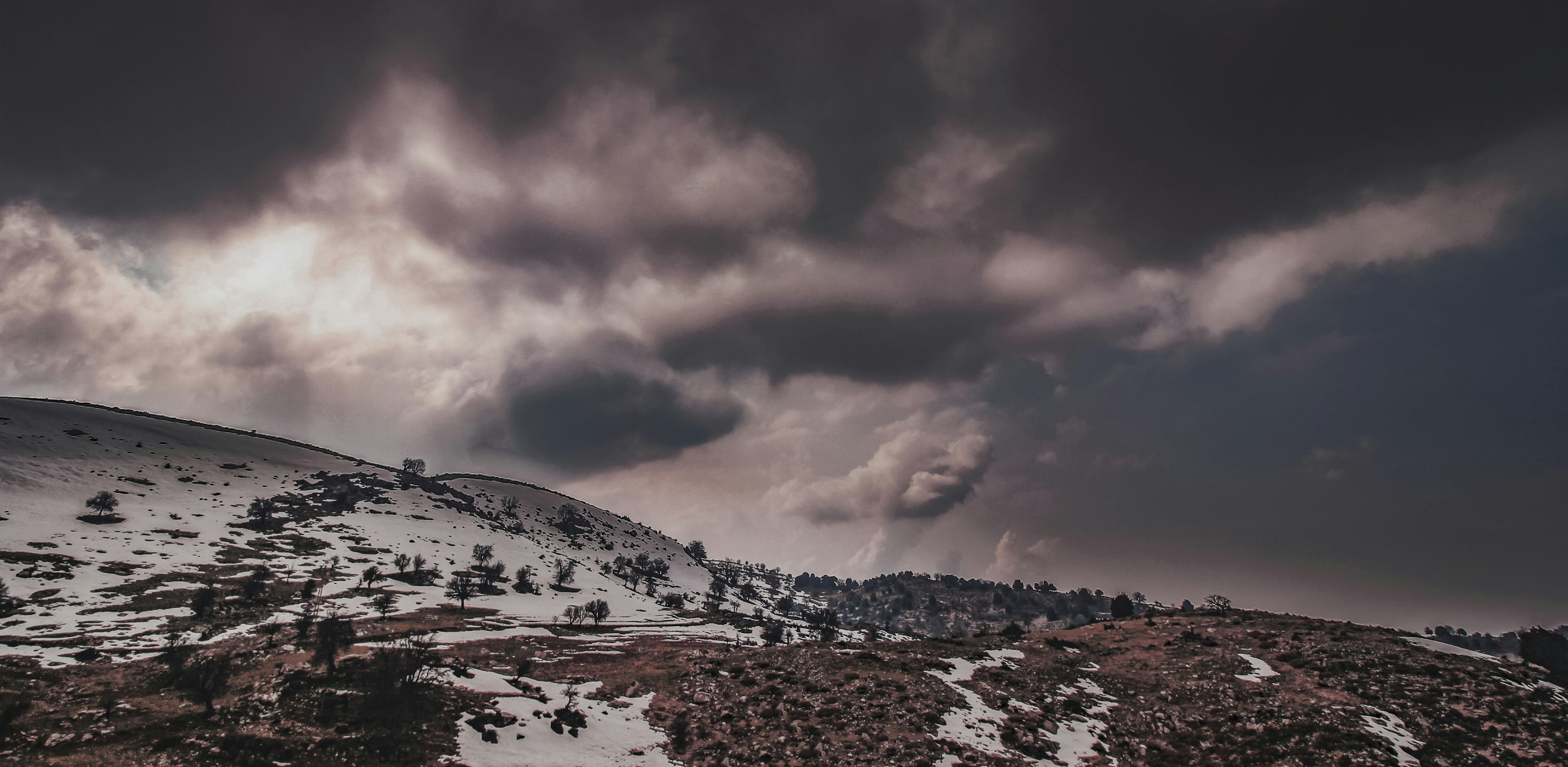 Stormfront on the Ridge: Snow-kissed Hill under Brooding Skies
