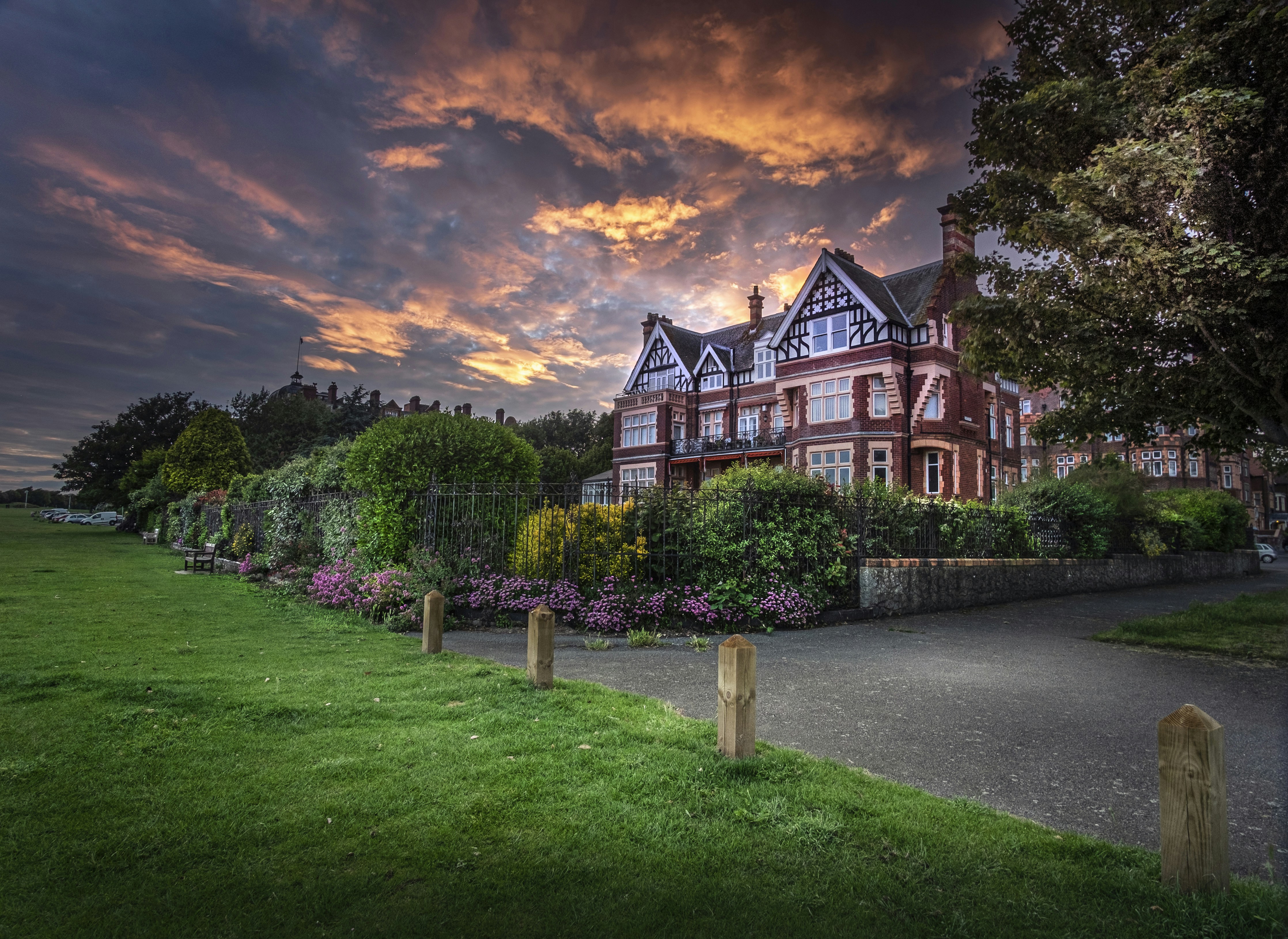 Victorian-style mansion surrounded by lush gardens and vibrant flowers at twilight, showcasing the interplay of architecture and nature.