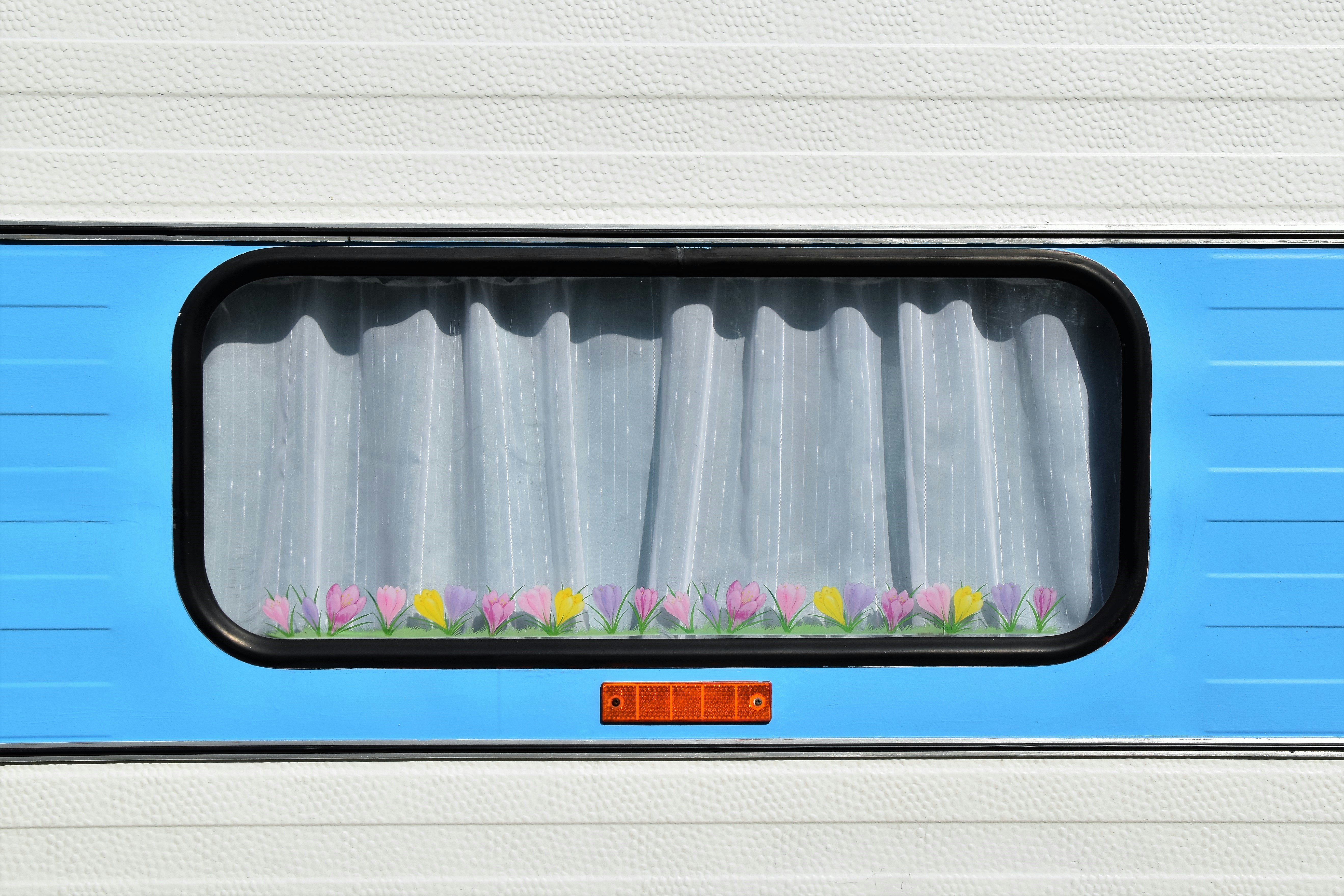 Bright blue caravan window adorned with a floral curtain featuring colorful tulips. A cheerful scene that invites curiosity.