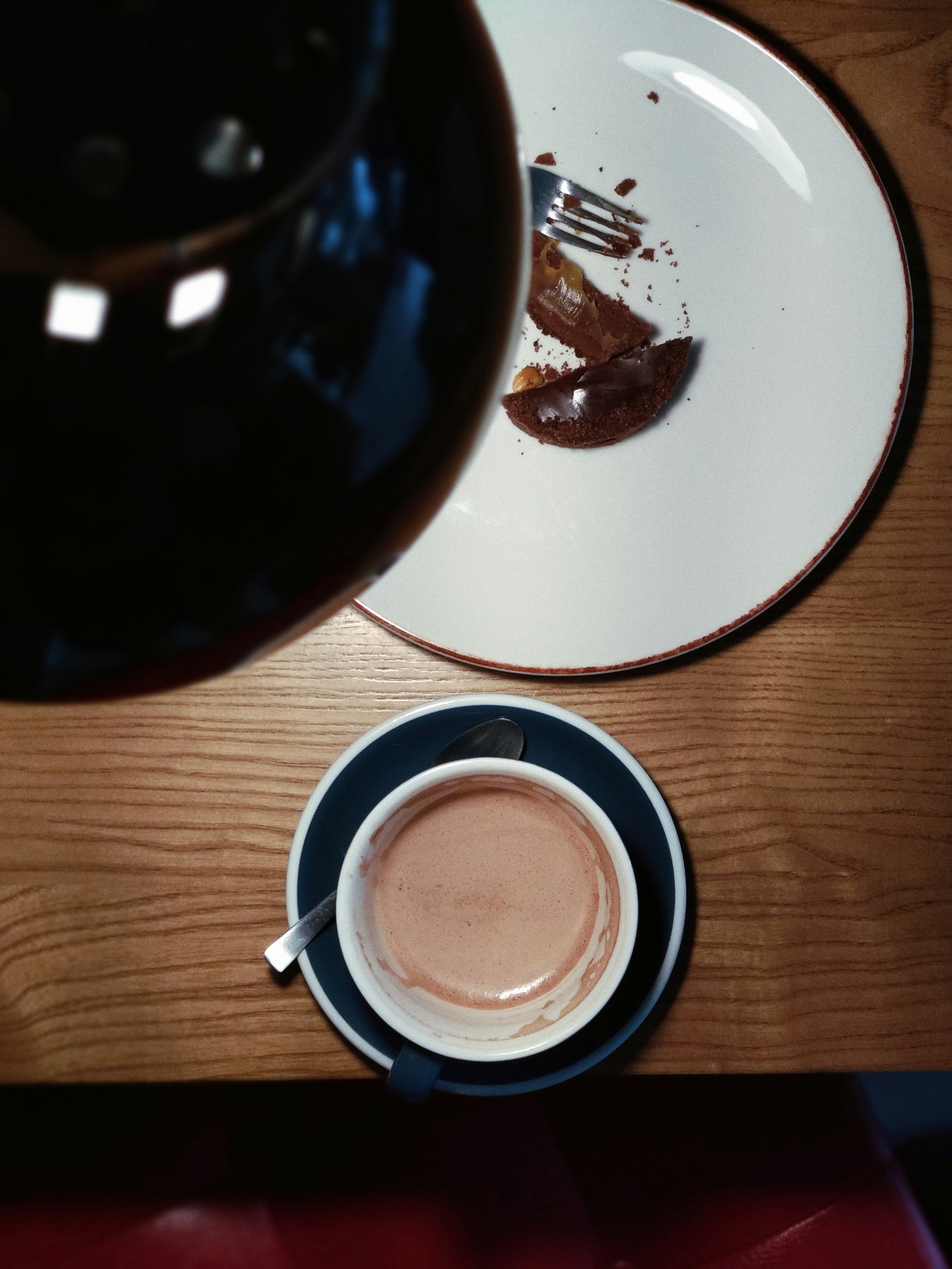 Half-eaten dessert on a white plate with a coffee cup on a wooden table under a hanging lamp.