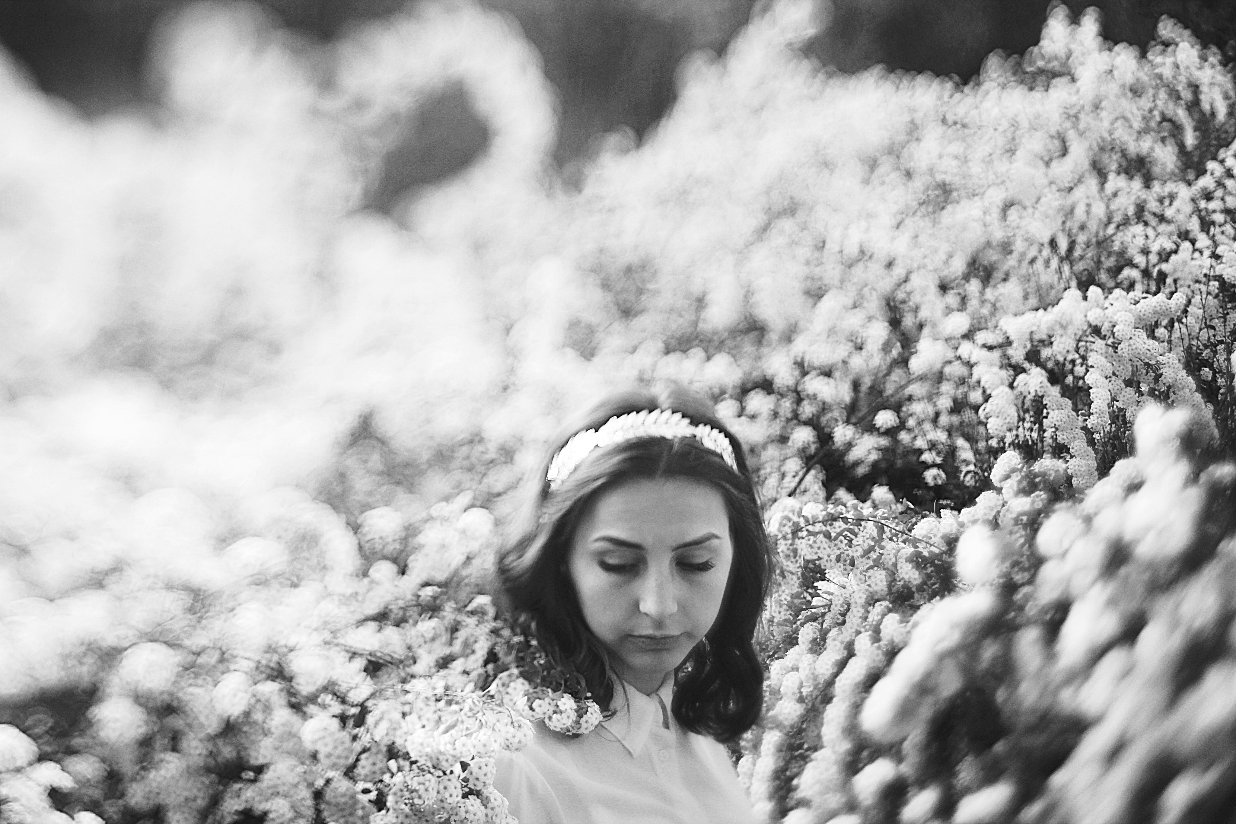 grayscale photography of woman standing near flowers