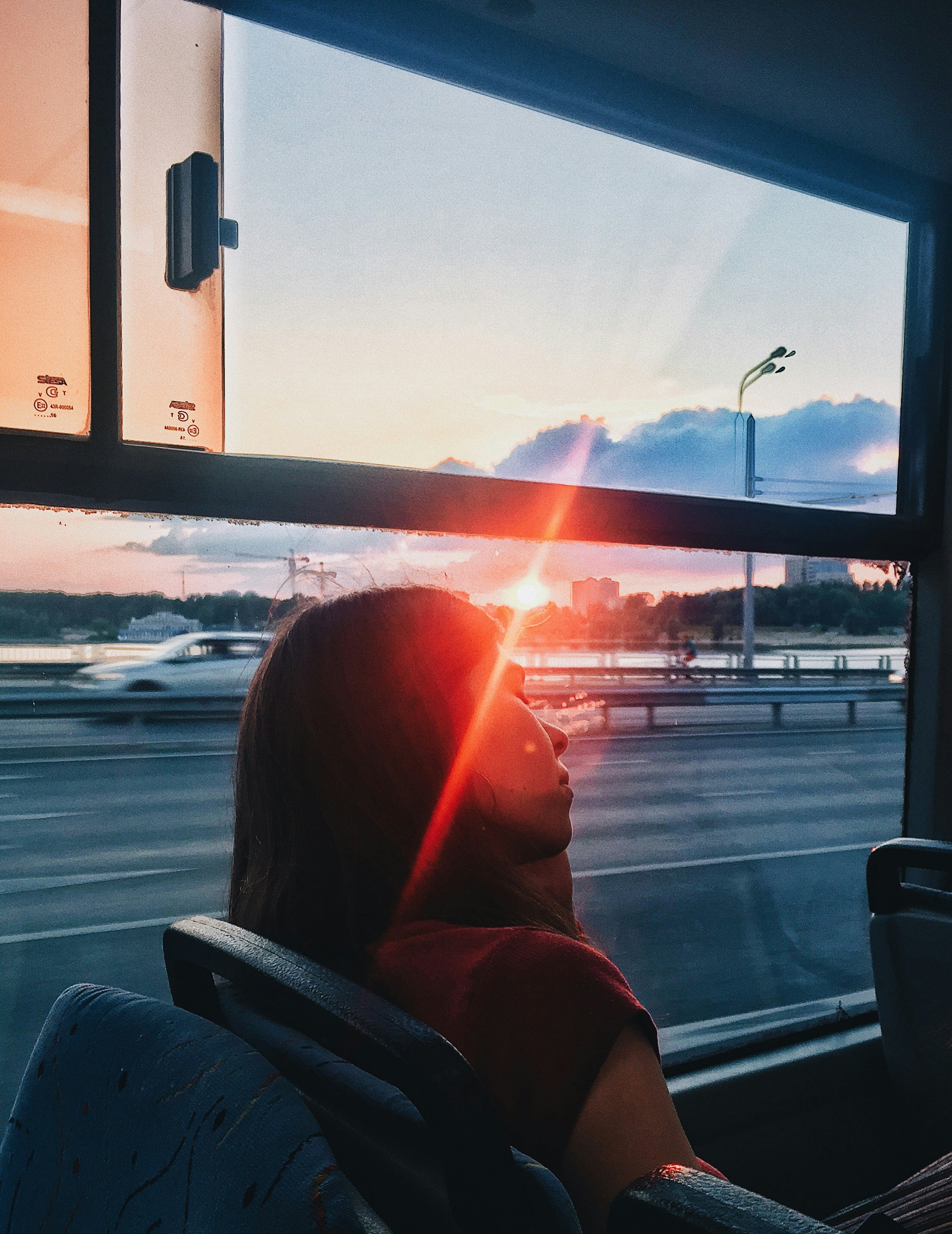 Sunset Transit: Silhouette bathed in a red lens flare aboard a moving bus