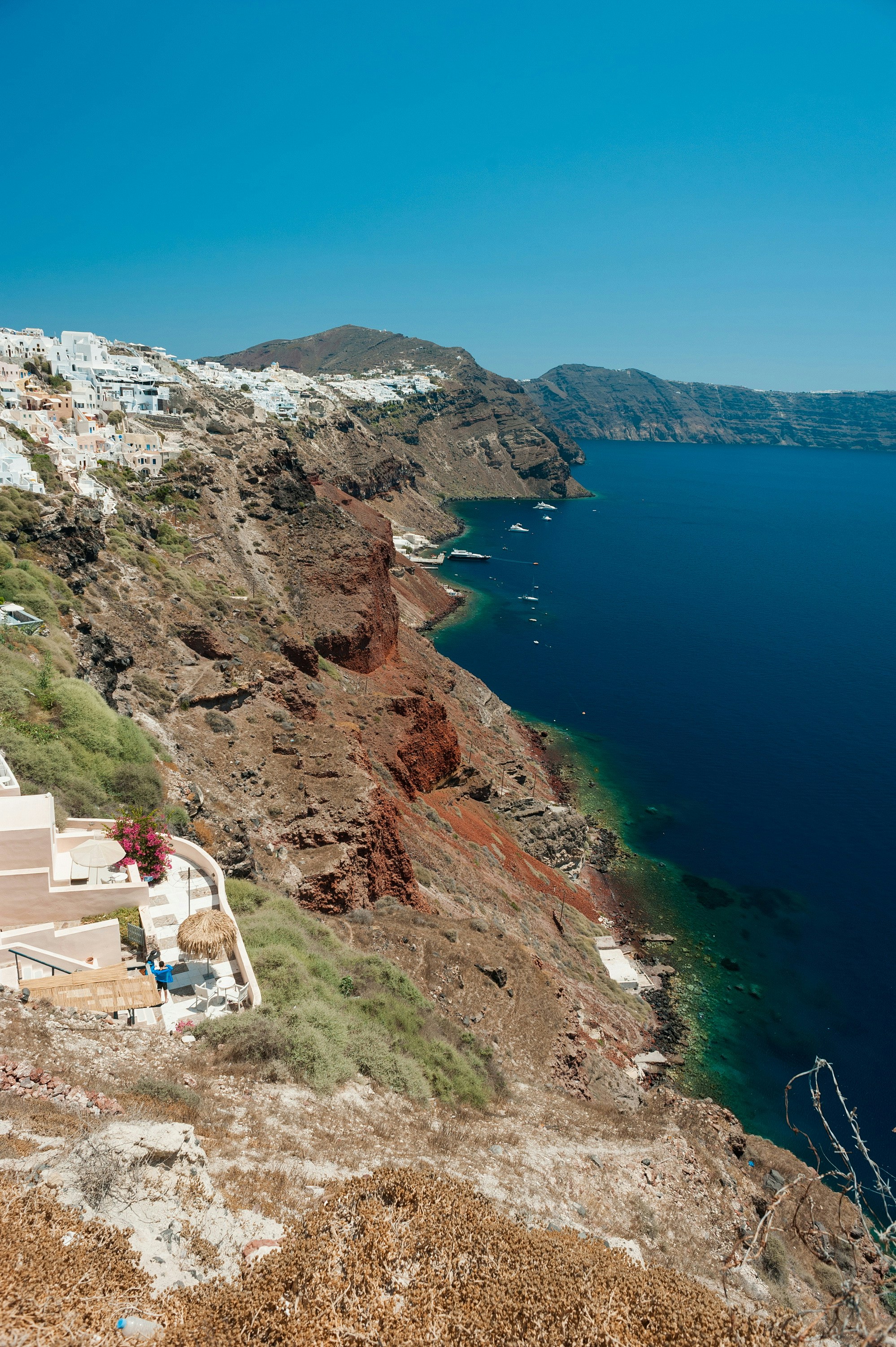 Whitewashed terraces cling to red cliffs above a sapphire sea