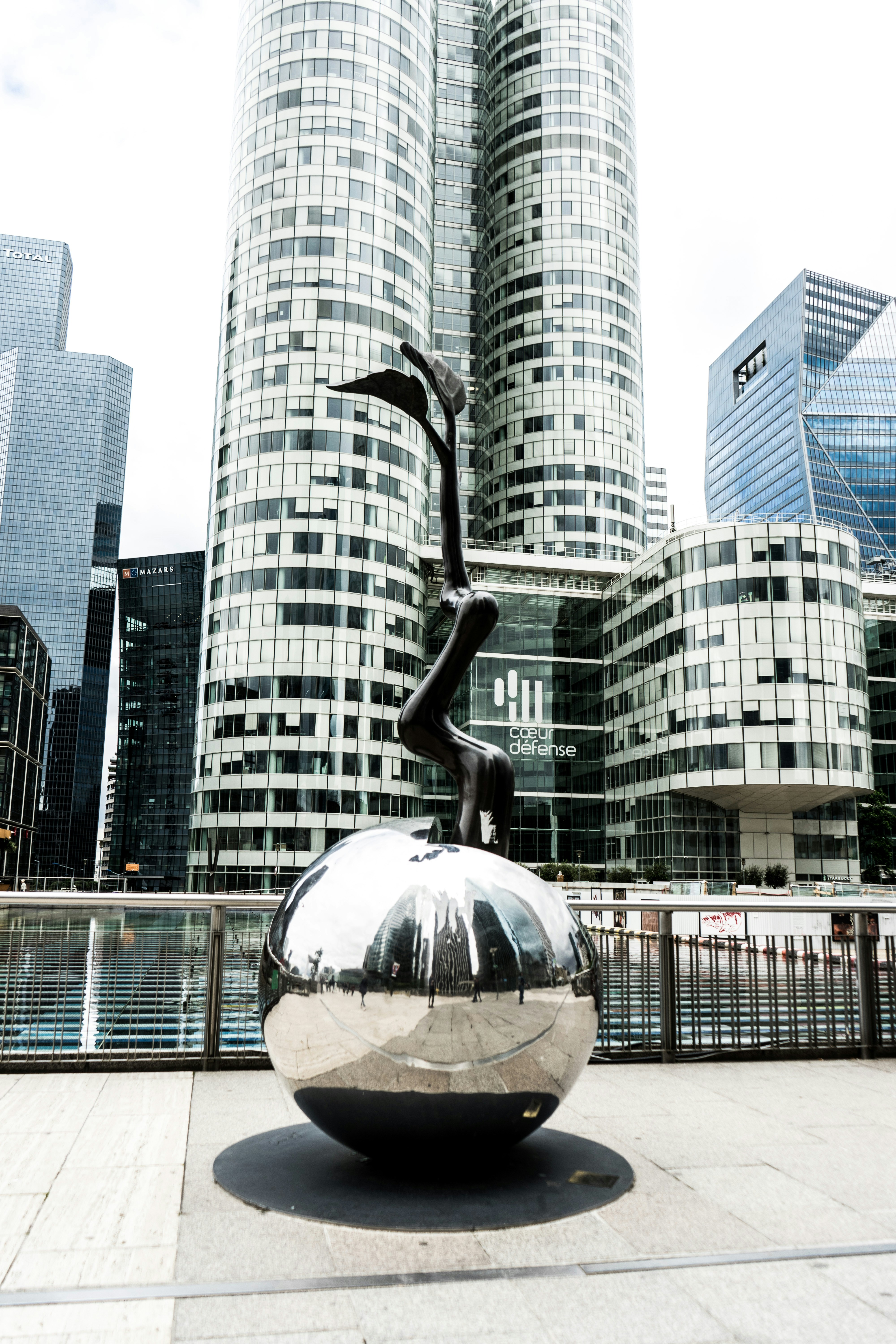 Chrome Orb Ballet: A Sculpted Figure Crowned by a Reflective Sphere Amid Glass Giants