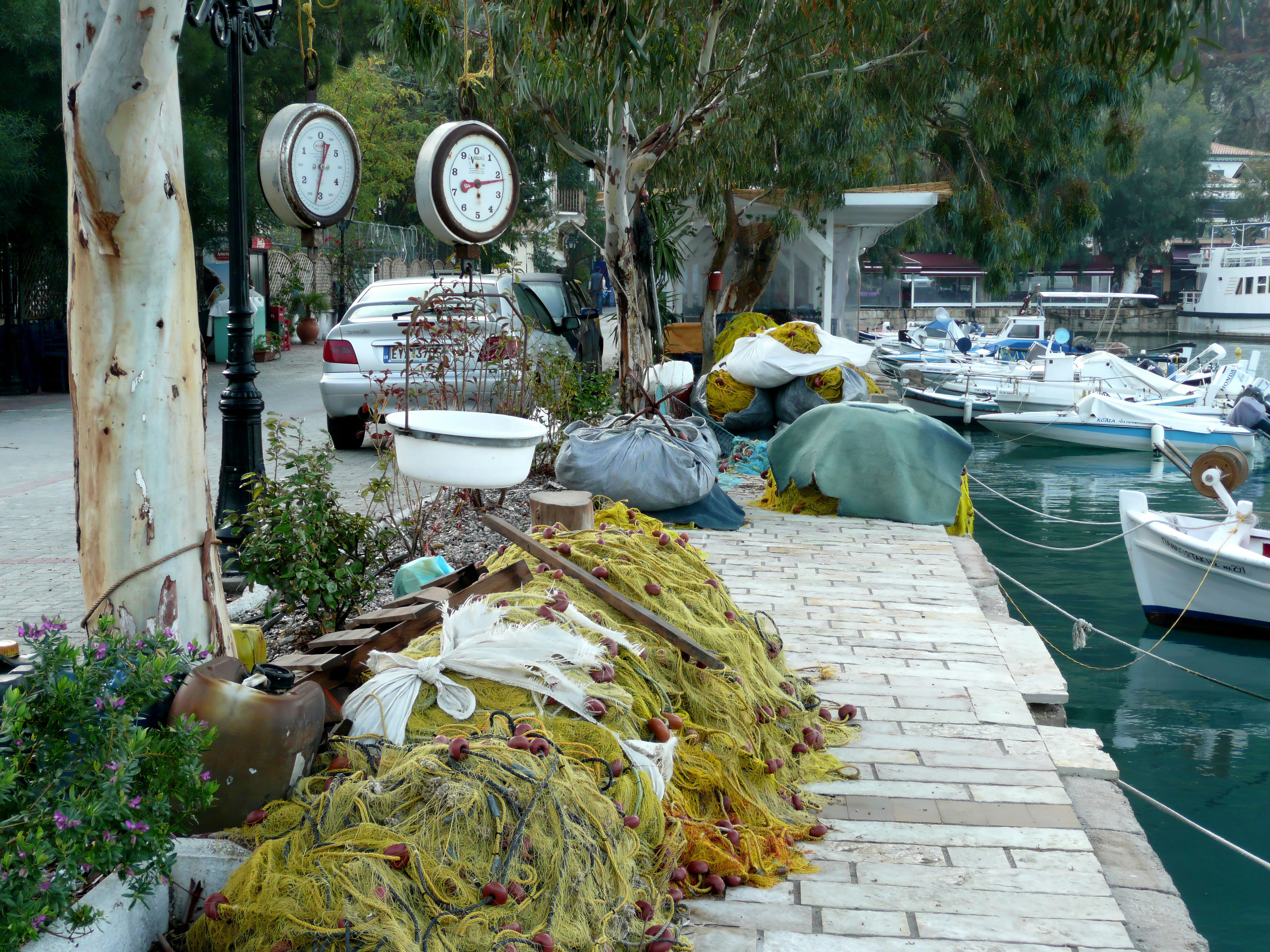 Weathered fishing nets and ropes spill along the stone quay beside moored boats in a calm harbor. A working harbor scene that emphasizes gear and vessels.