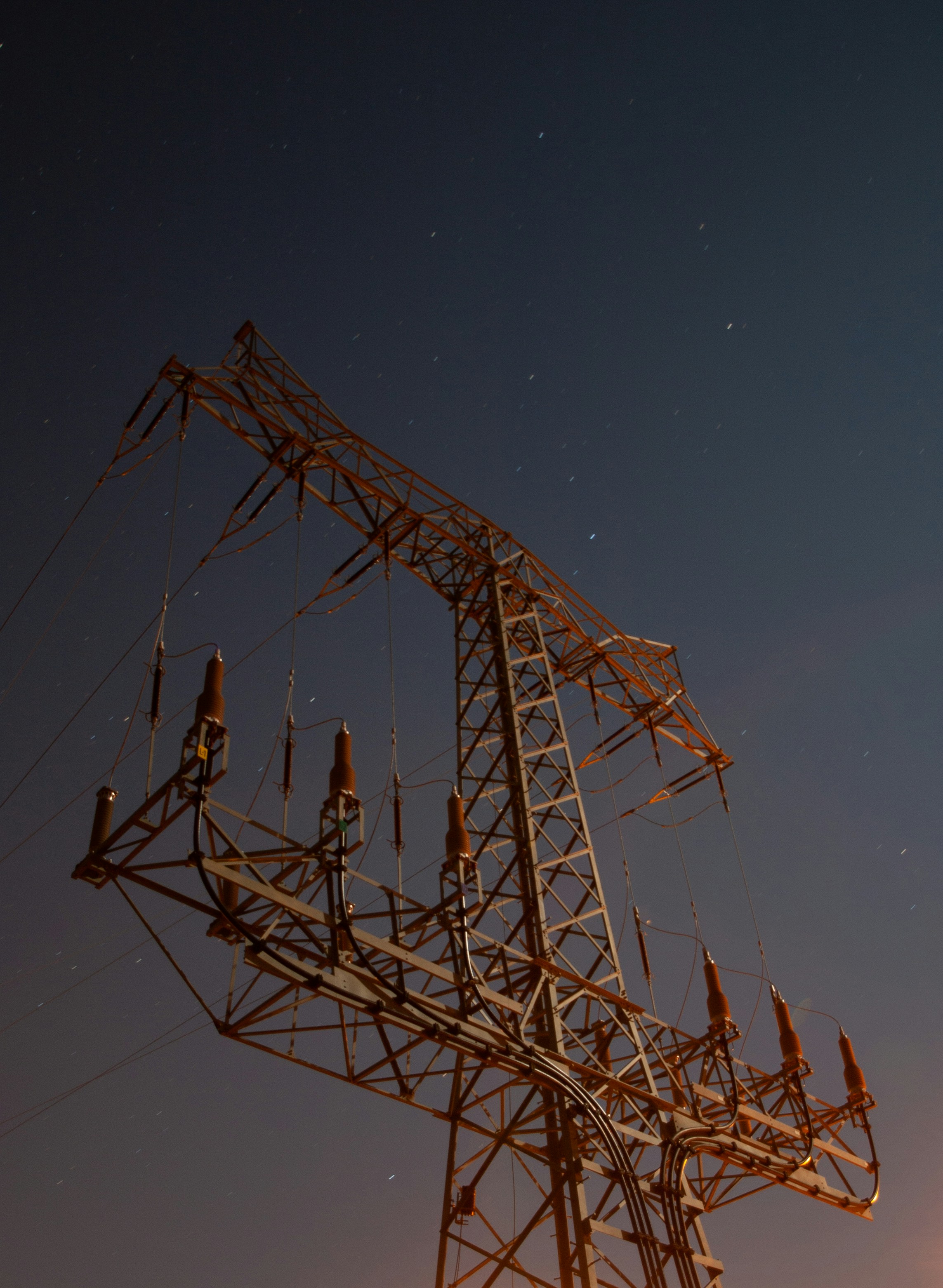 Night photograph of a metal transmission tower silhouetted against a star-filled sky.