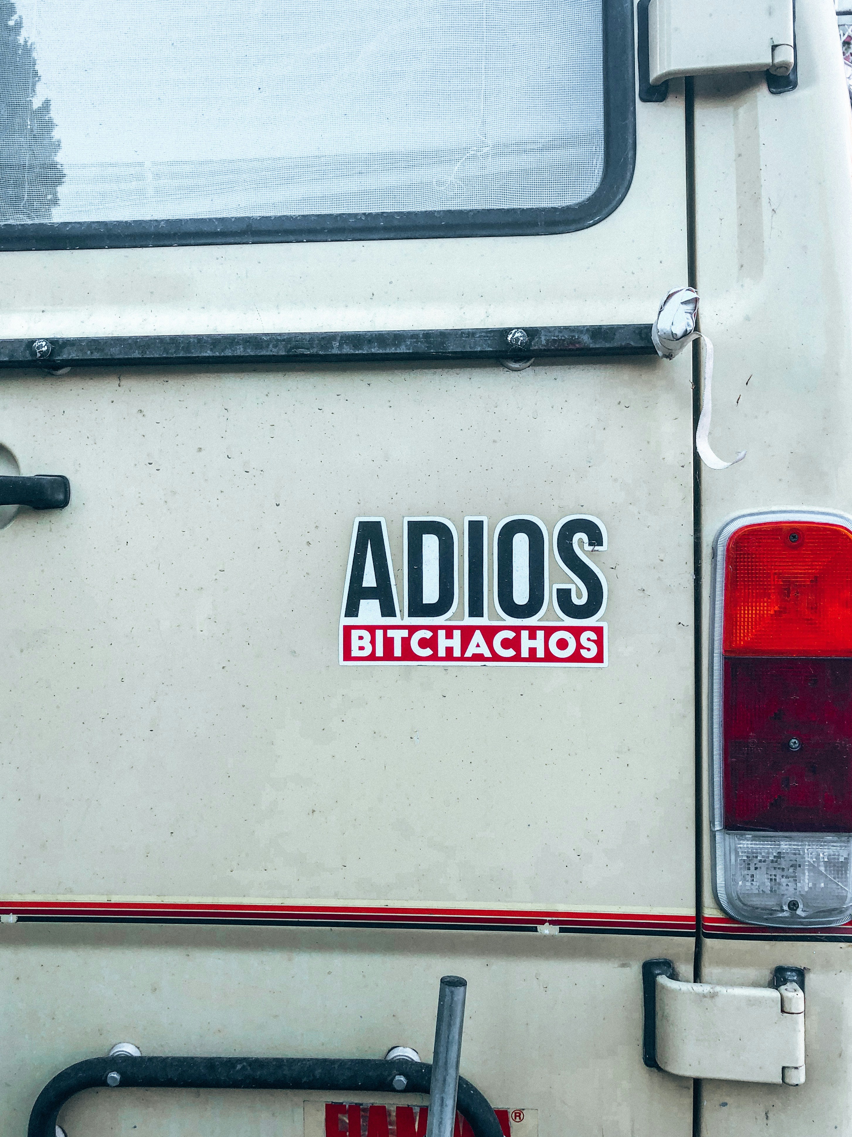 A humorous sticker reading 'ADIOS BITCHACHOS' affixed to the rear of a vintage vehicle, showcasing its playful character.