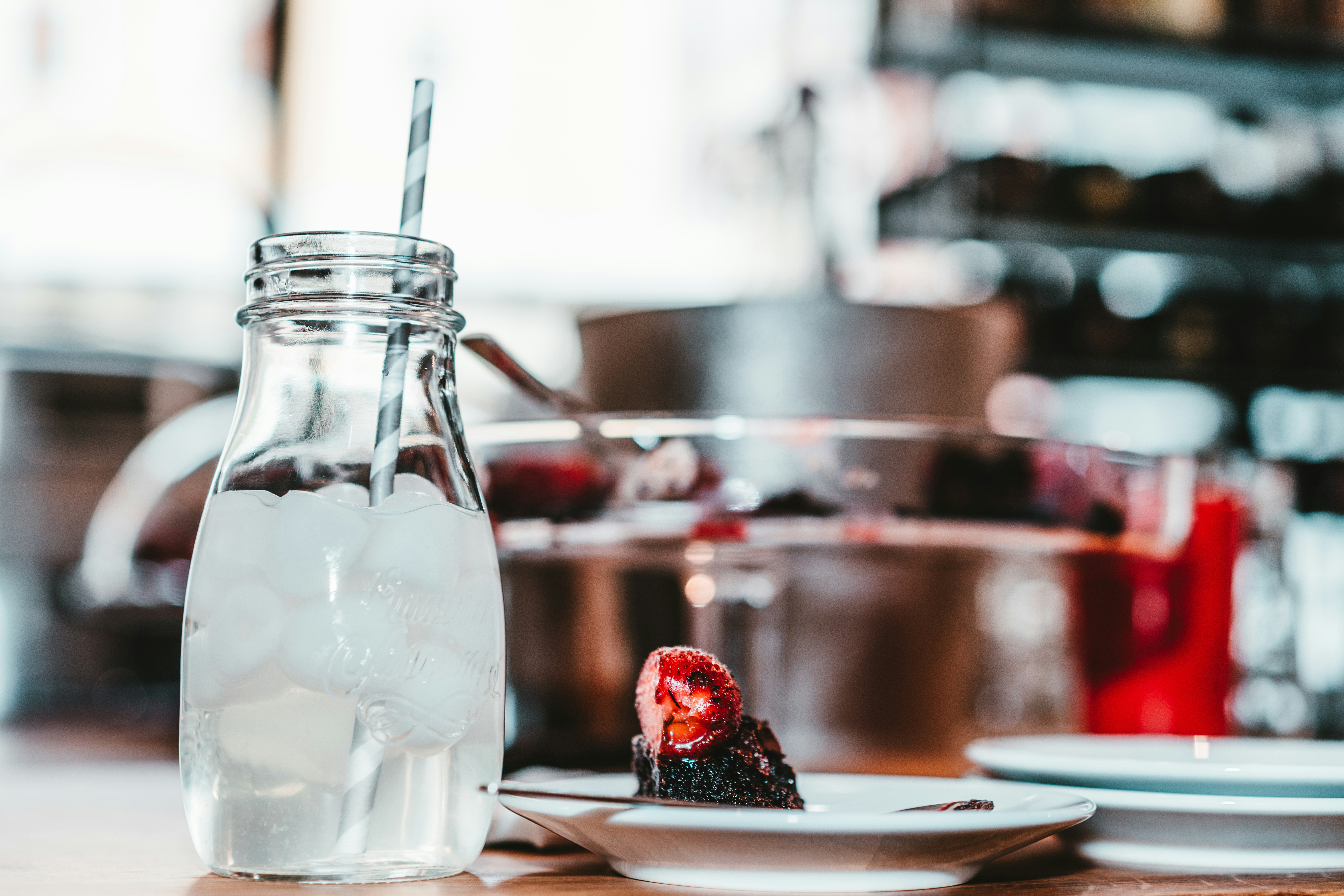 A glass of water with ice sits beside a slice of chocolate cake topped with a strawberry, capturing a moment of indulgence in a cozy setting.