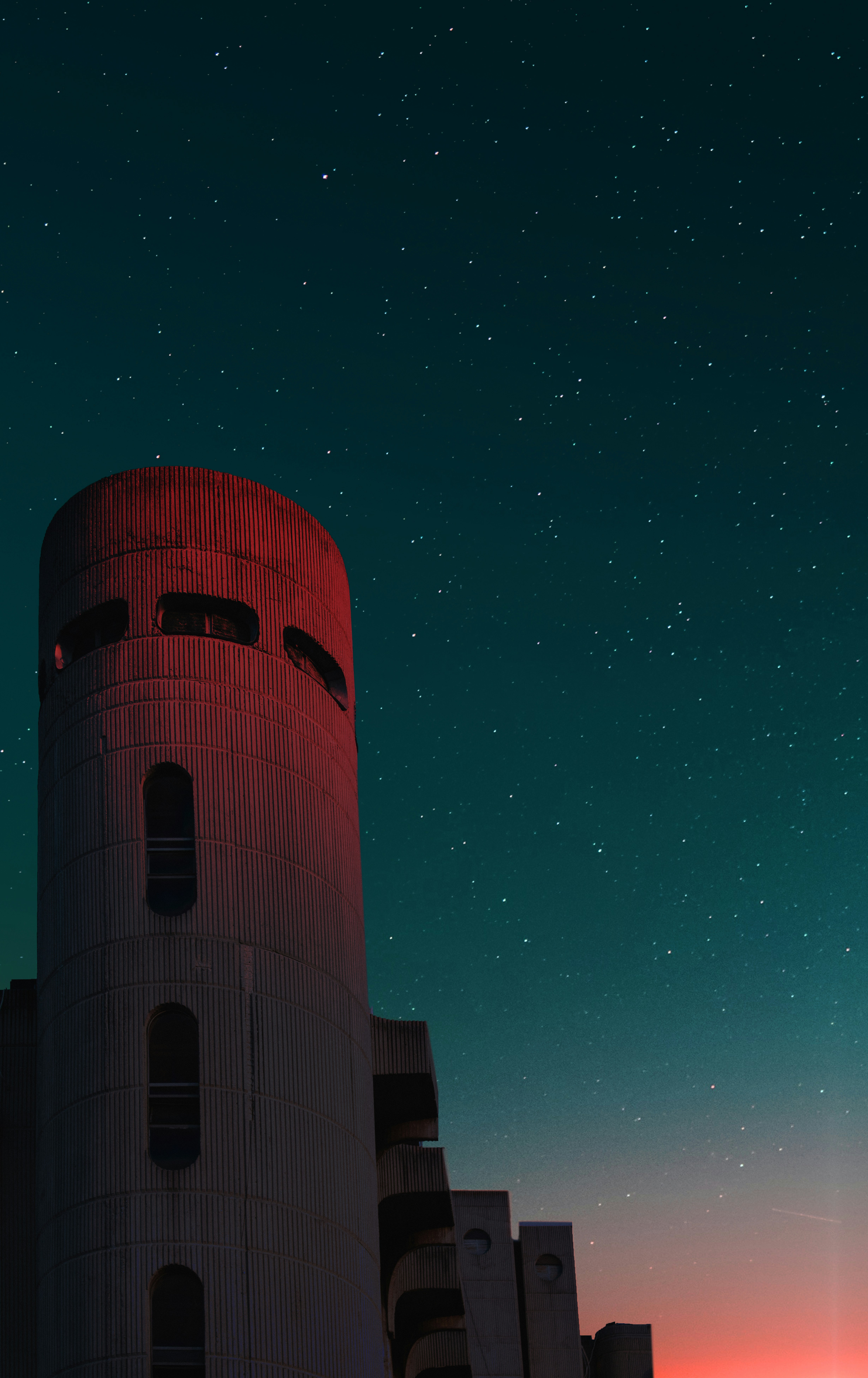 A uniquely shaped tower illuminated in red stands against a starry night sky, capturing the contrast between architecture and the cosmos.