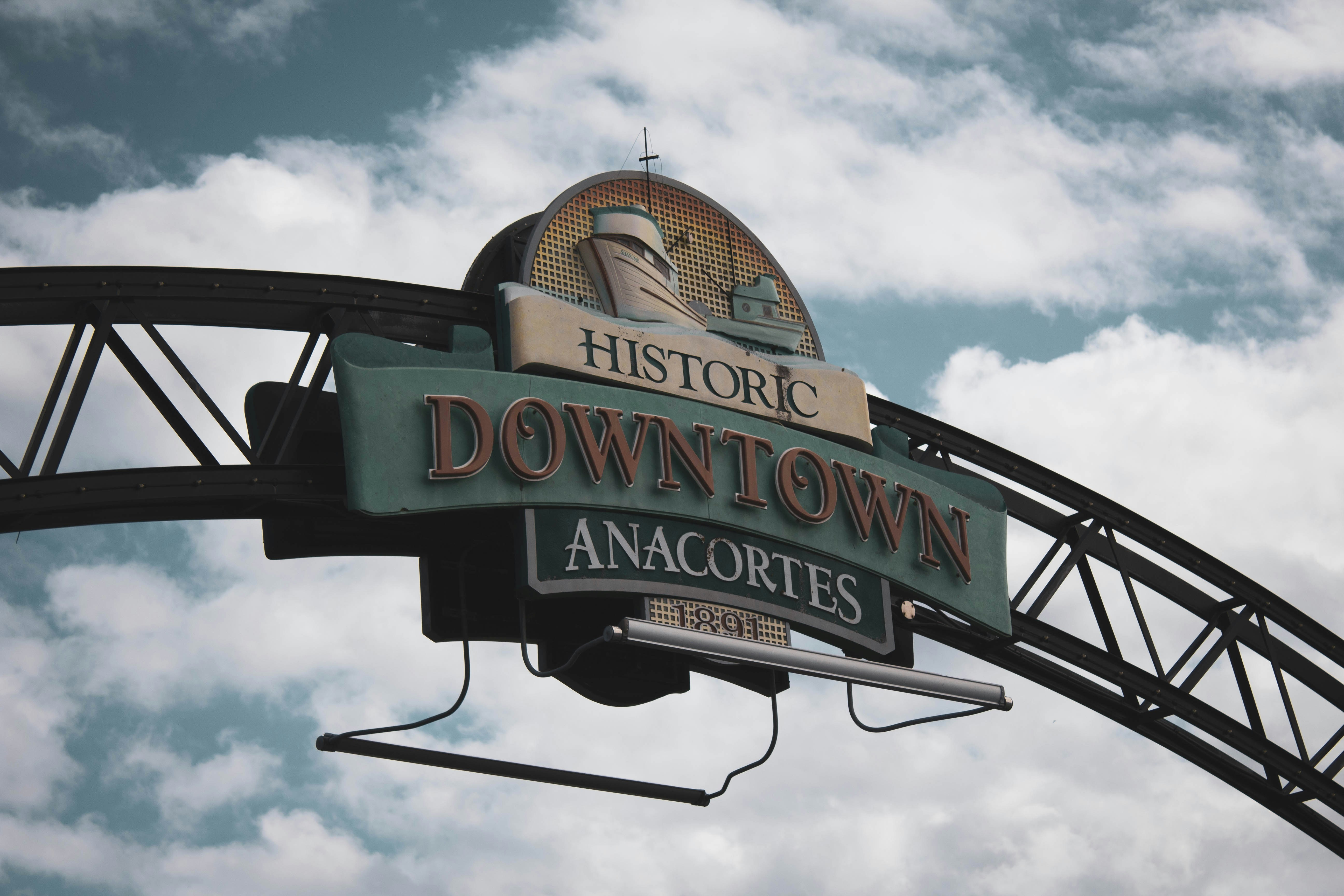 Sign archway marking the entrance to Historic Downtown Anacortes, featuring vintage design elements against a cloudy sky.