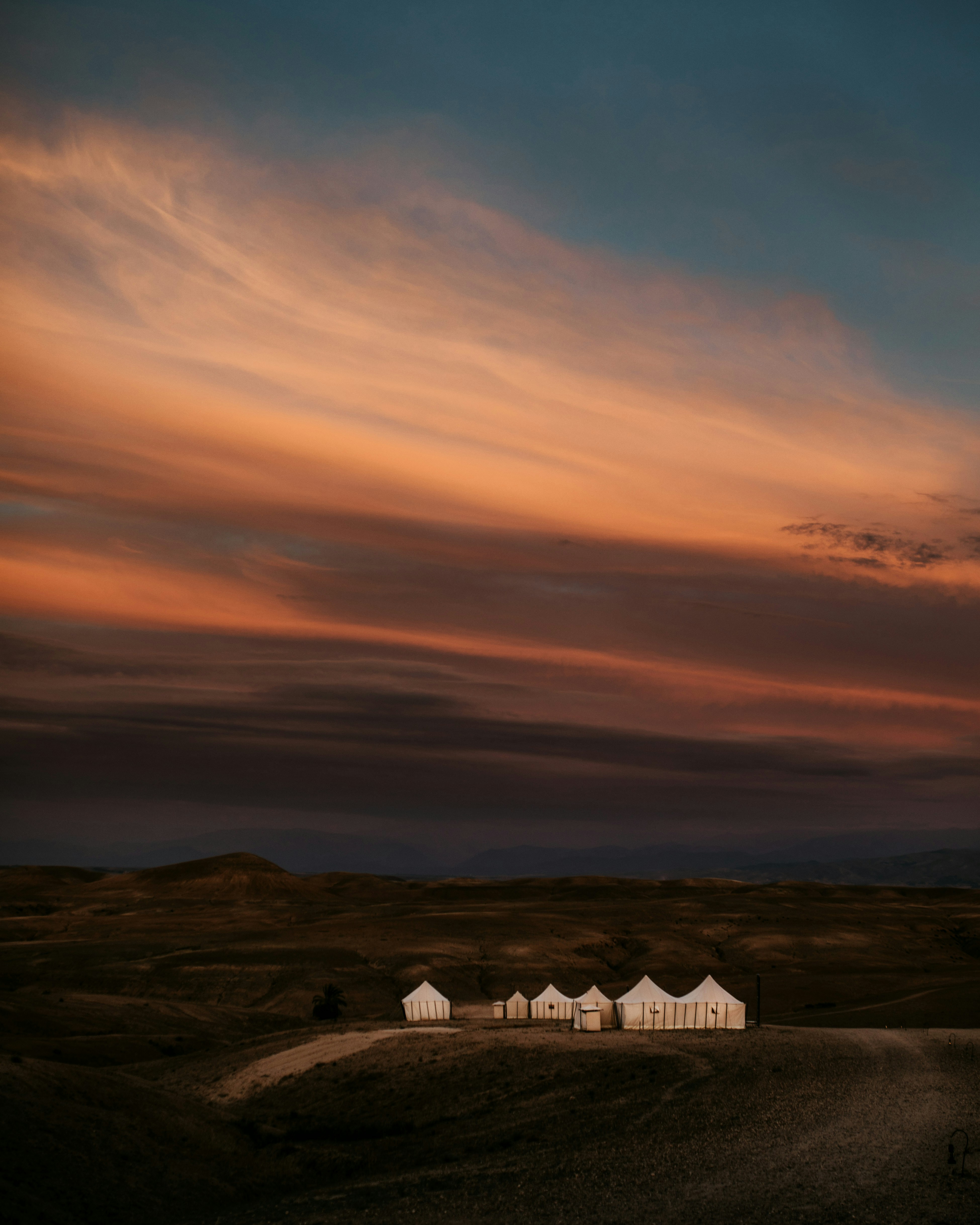 White tents nestled in rolling hills under a vibrant sunset sky, showcasing a blend of warm and cool hues.