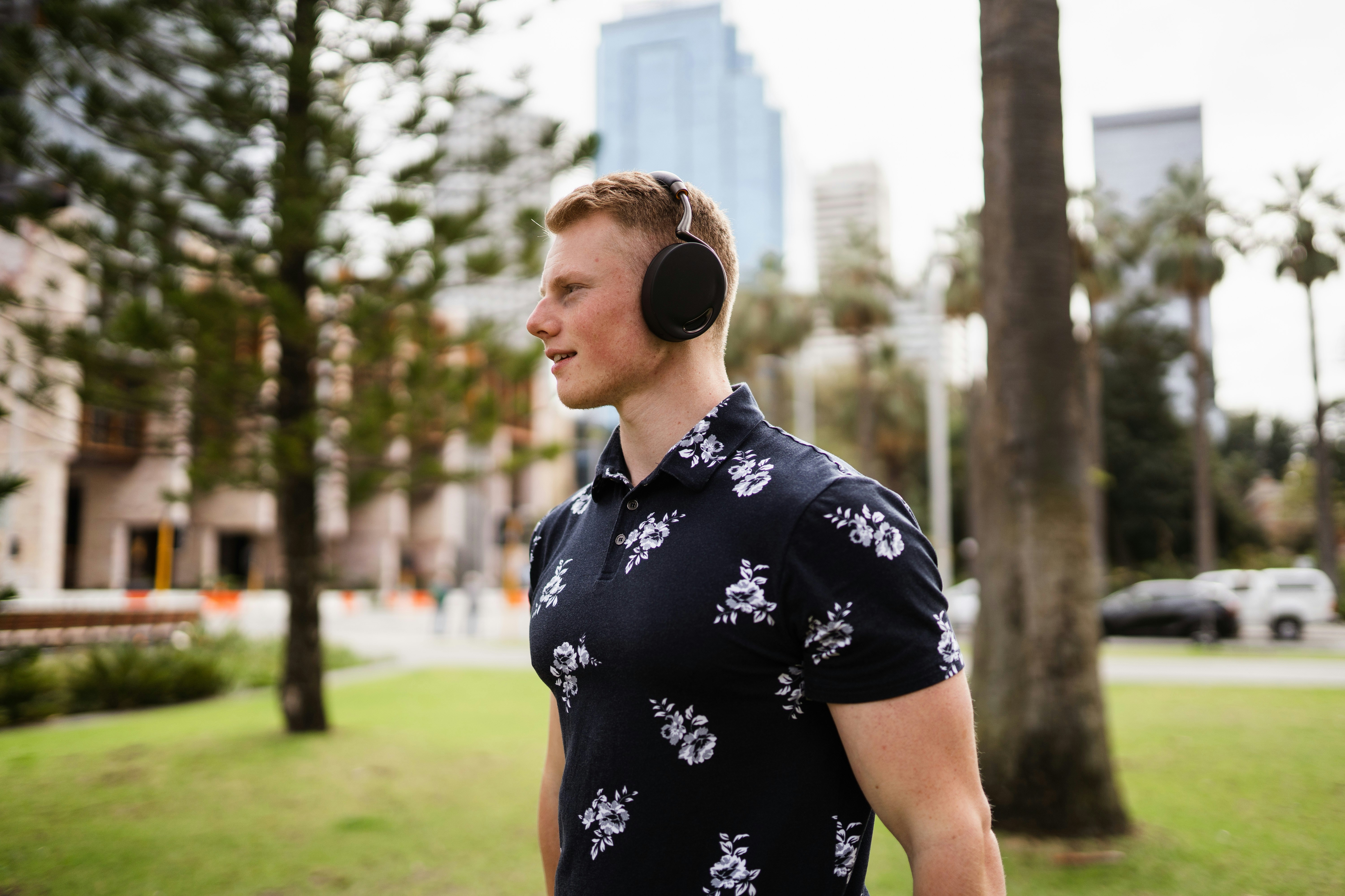 Man wearing headphones walks through a city park with skyscrapers in the background.