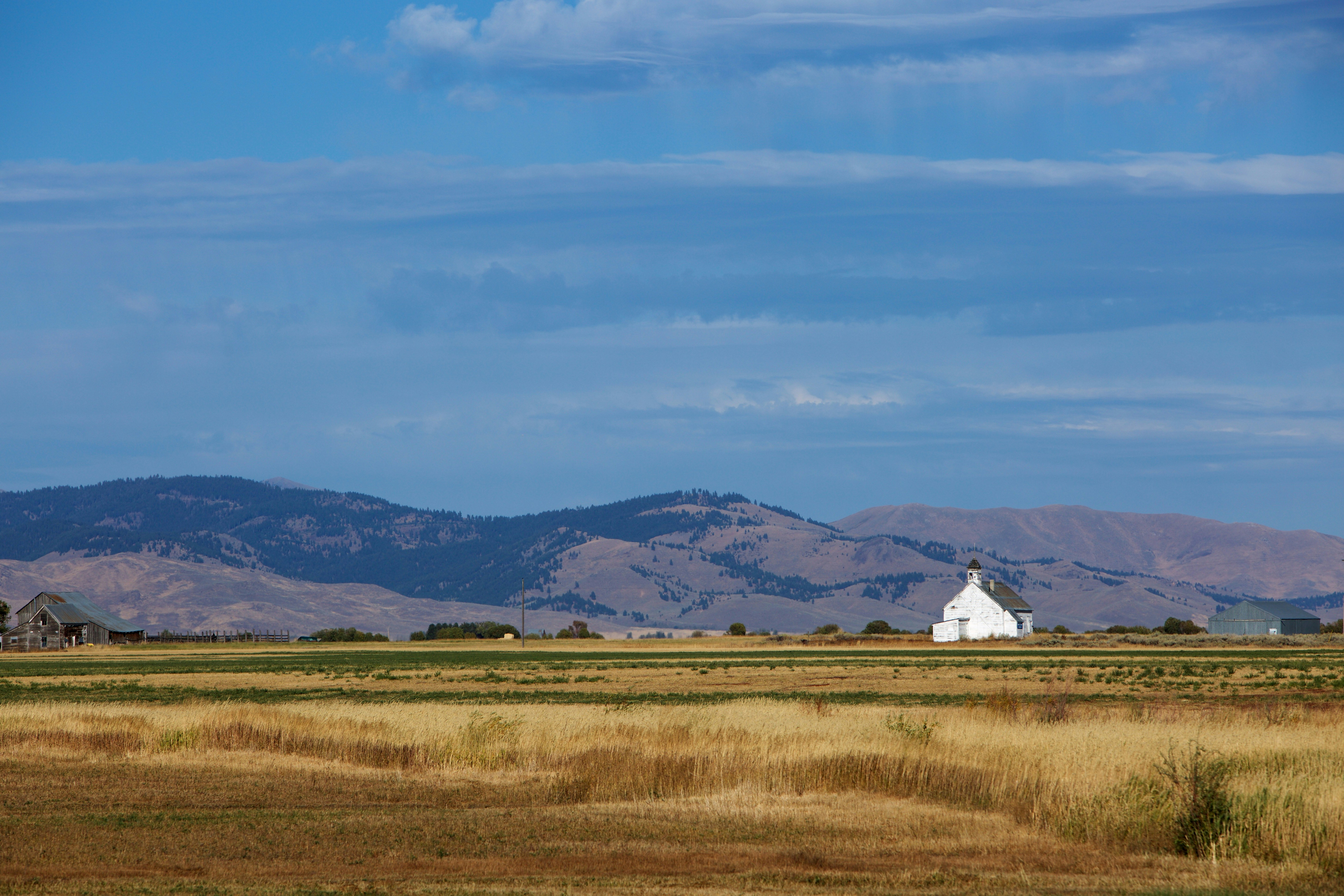 White wooden church set against rolling hills and expansive fields under a vast blue sky.