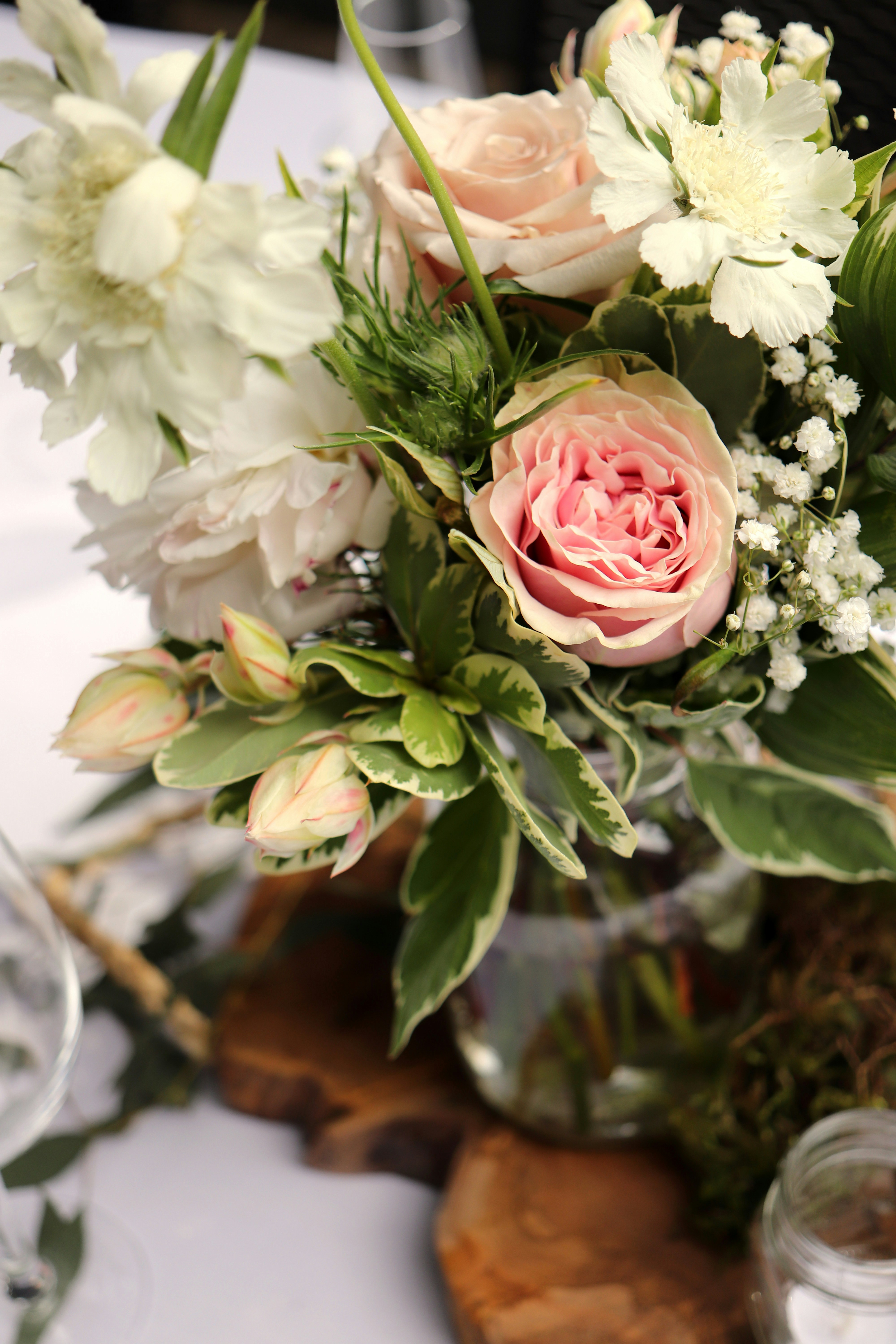 A beautifully arranged bouquet featuring pink roses, white flowers, and lush greenery, set against a rustic wooden backdrop.