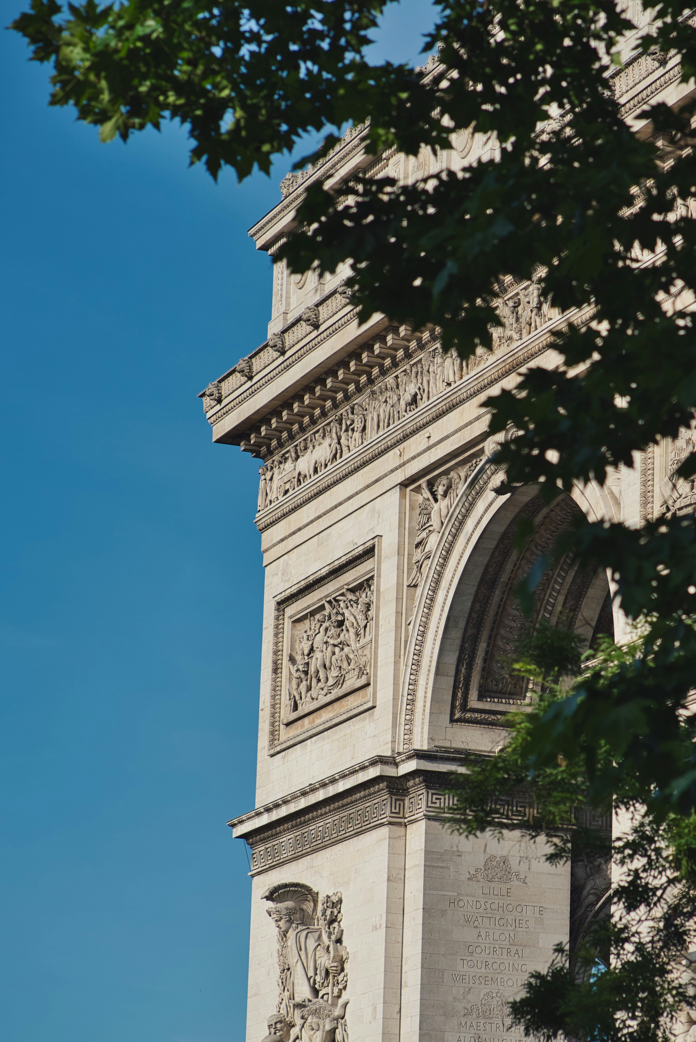 Leaf-Framed Arc de Triomphe Facade: Sunlit Carvings in Clear Sky