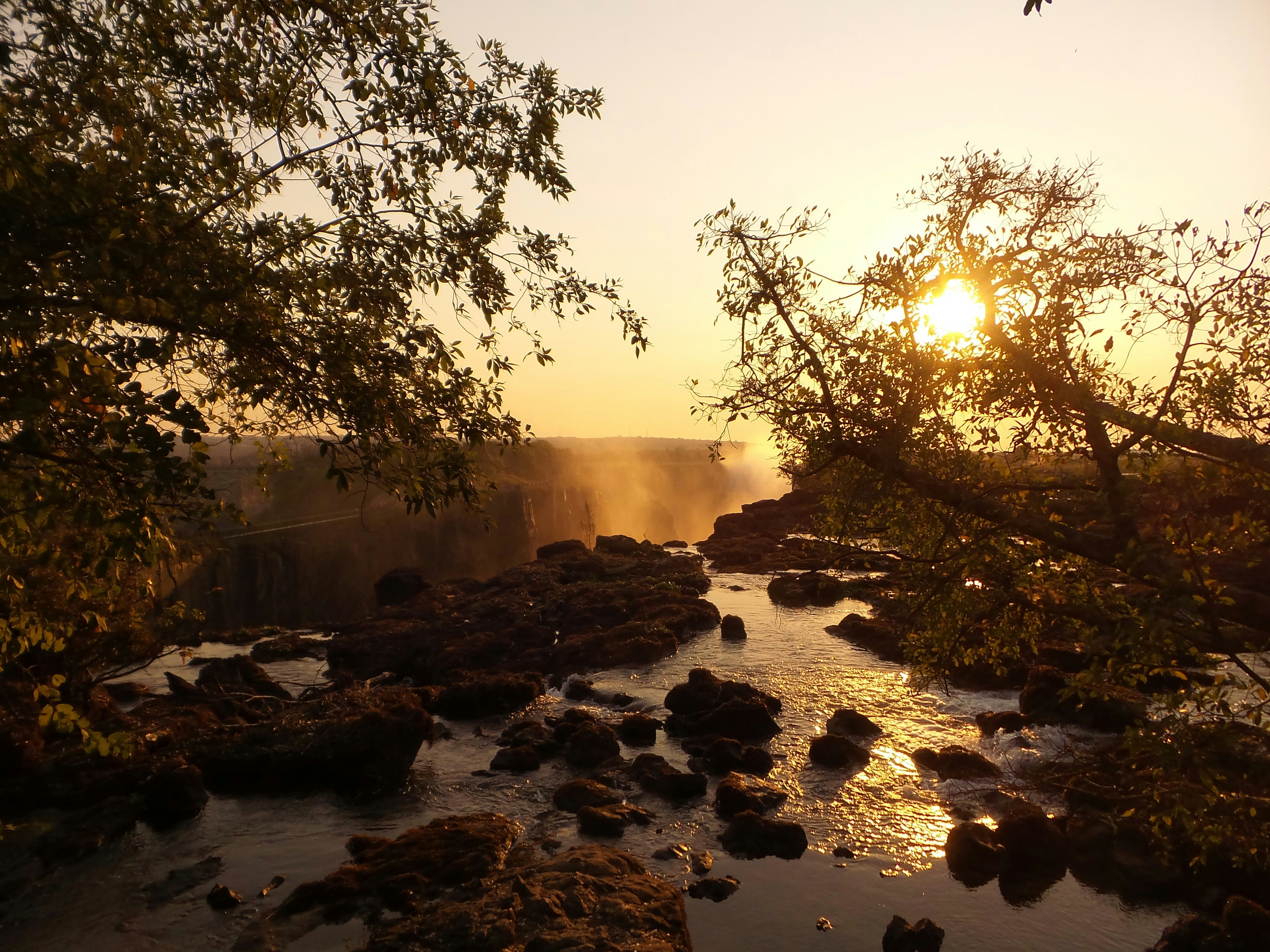 Sunset illuminating a waterfall surrounded by rocky terrain and foliage, creating a serene atmosphere.