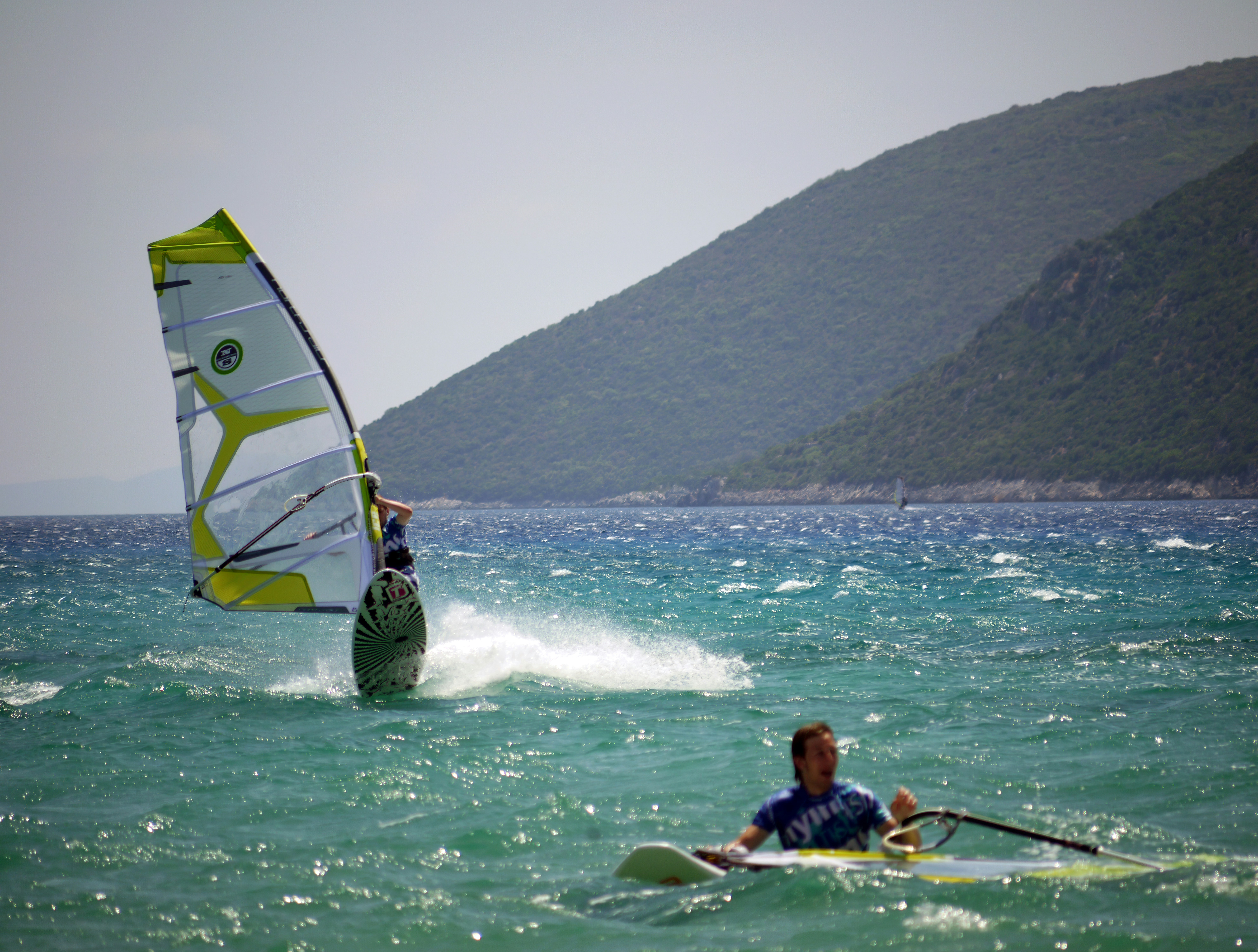 Neon Sail on Turquoise Wake: Windsurfers Against a Backdrop of Green Hills