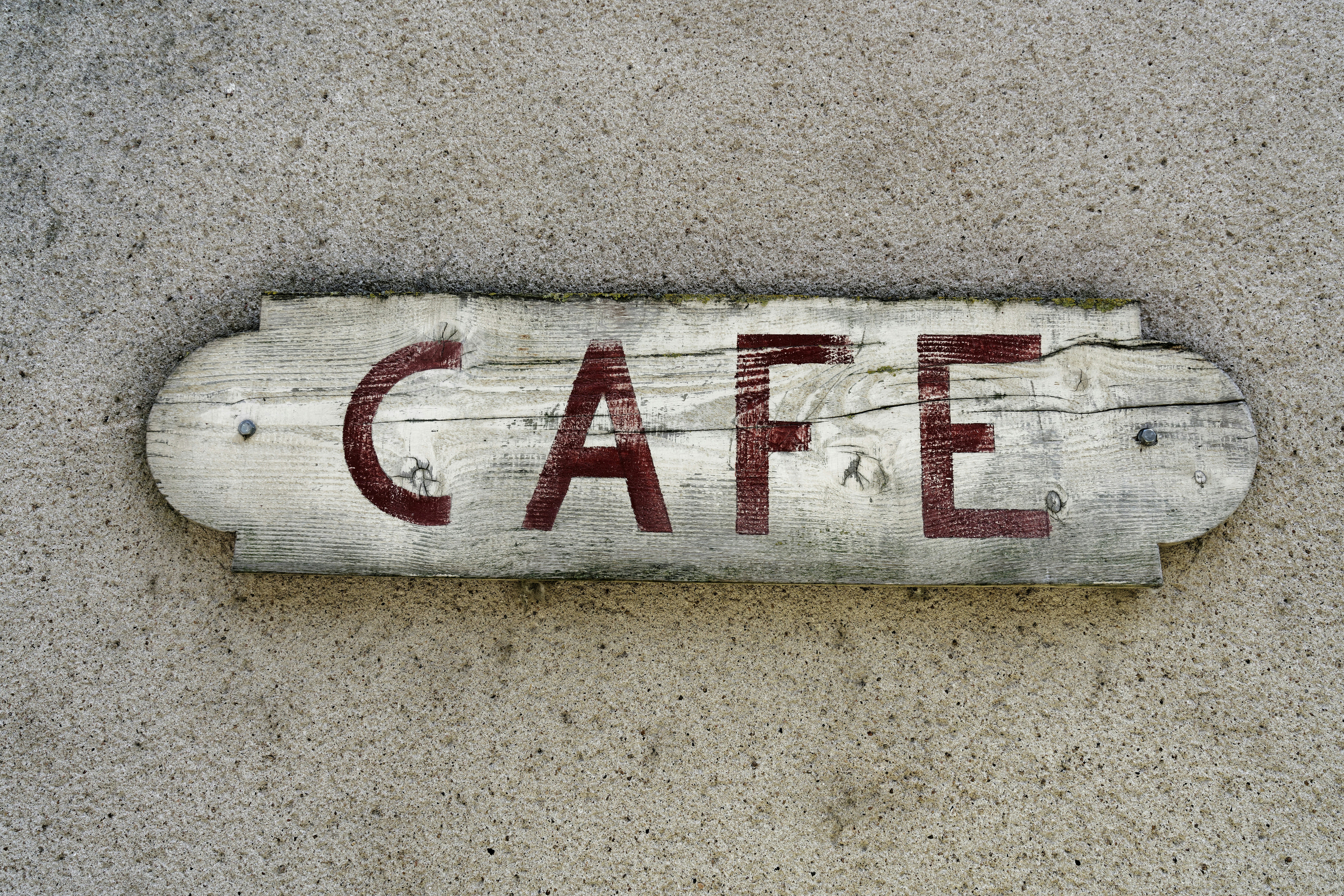 Weathered Cafe Sign Anchored to a Textured Sand-Tone Concrete Wall