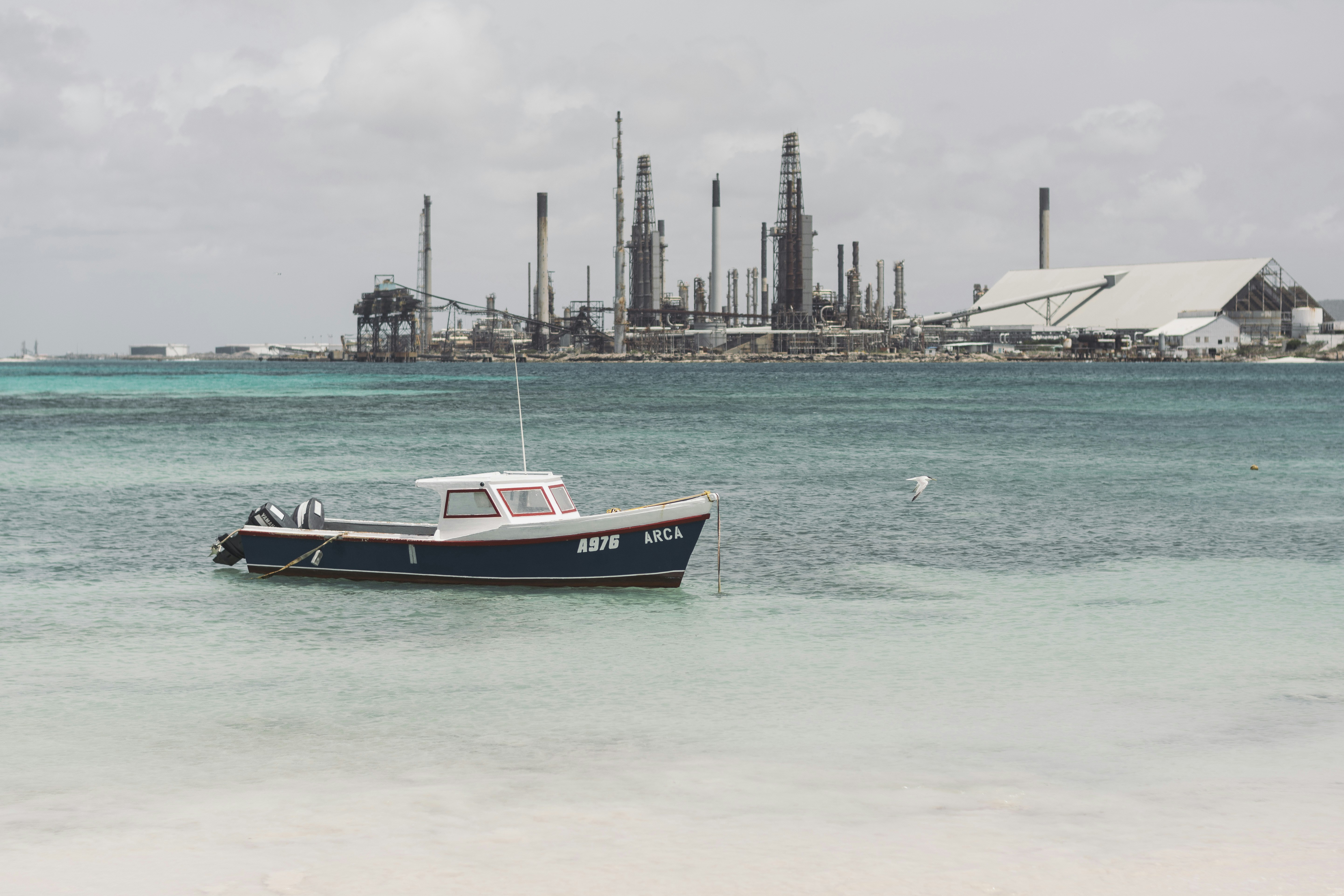 Turquoise Shoreline Pause: A Small Boat Against a Distant Industrial Horizon