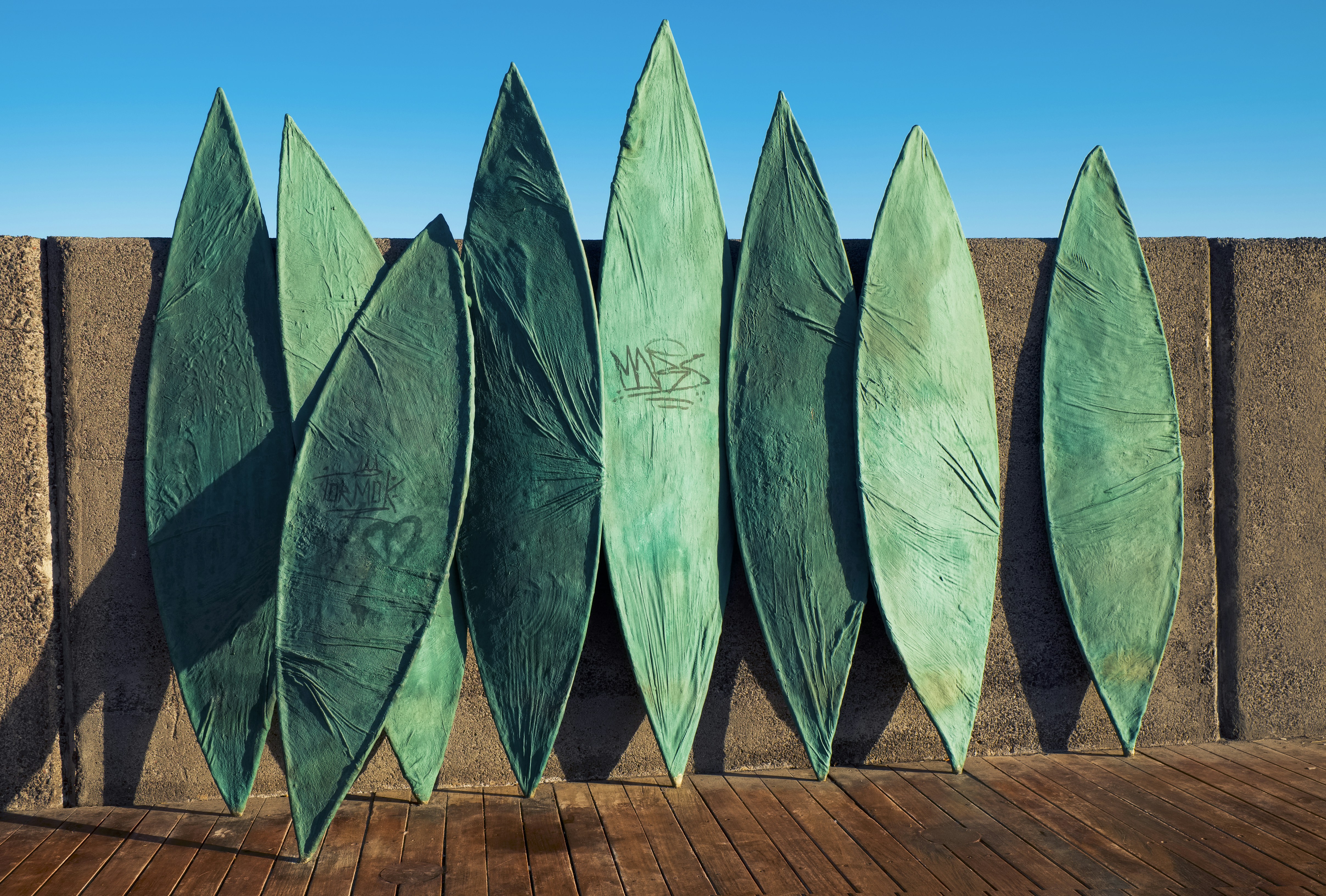 Verdant Spires: A Row of Green Surfboards Lean Against a Weathered Wall Under a Crisp Blue Sky