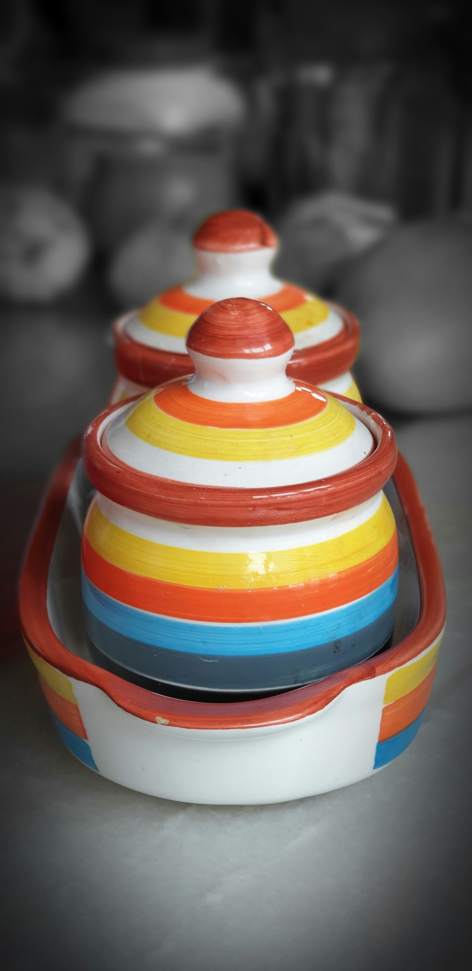 Colorful ceramic containers with striped patterns, set against a softly blurred background. The design emphasizes the playful use of color and form.